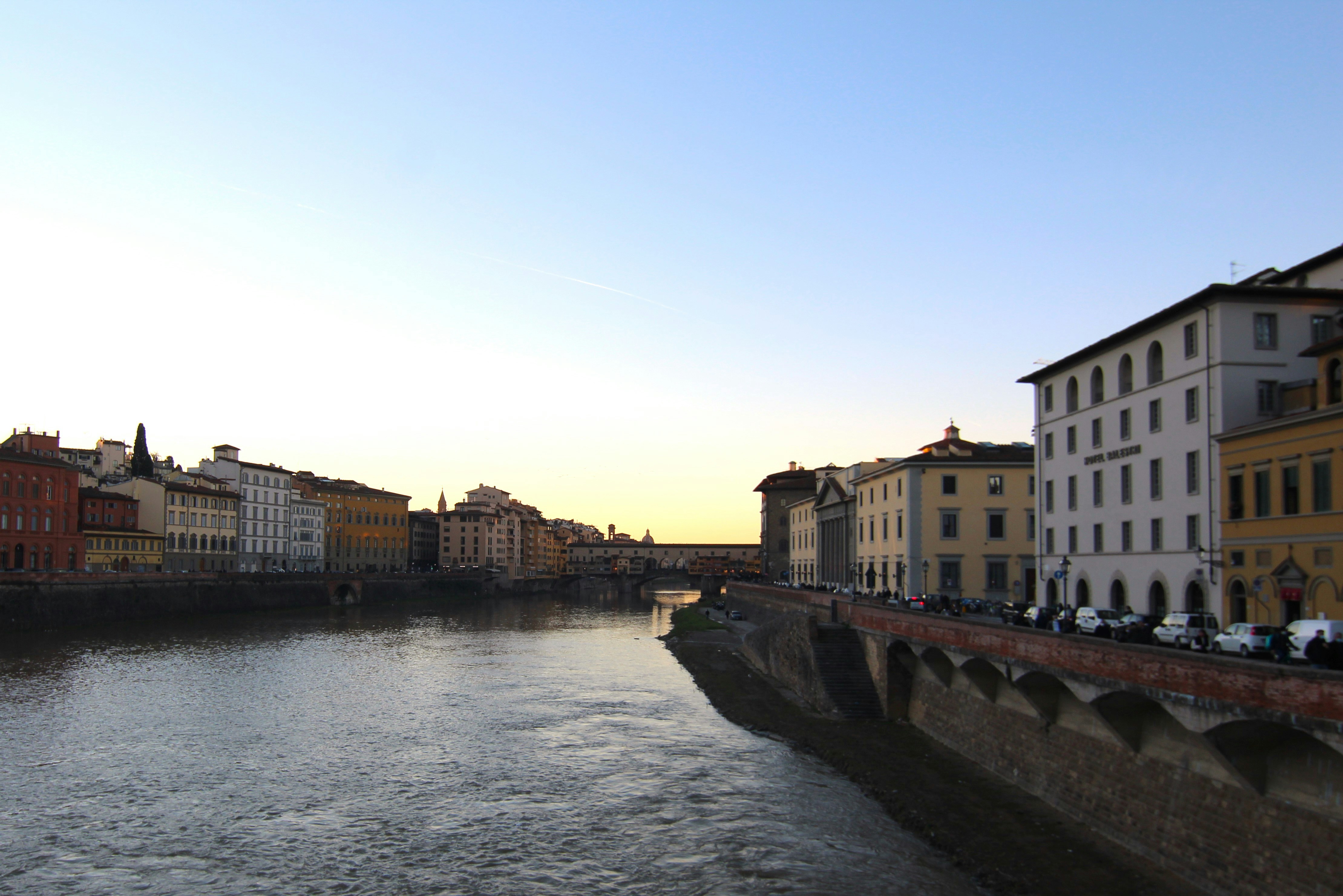 Historic buildings lining the Arno River under a serene twilight sky.
