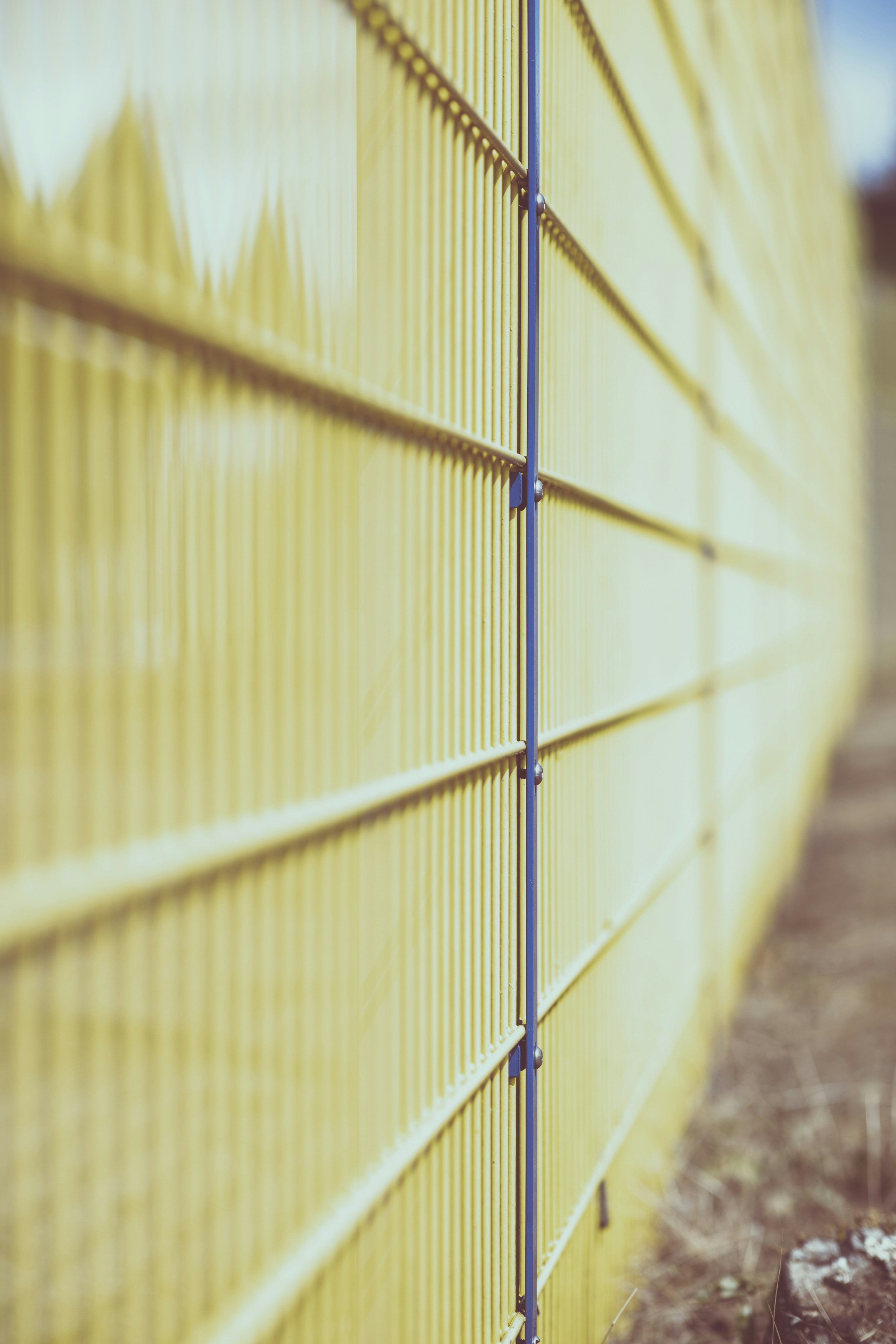A shallow depth-of-field shot of a long yellow ribbed wall with a blue vertical seam, creating a strong linear perspective.