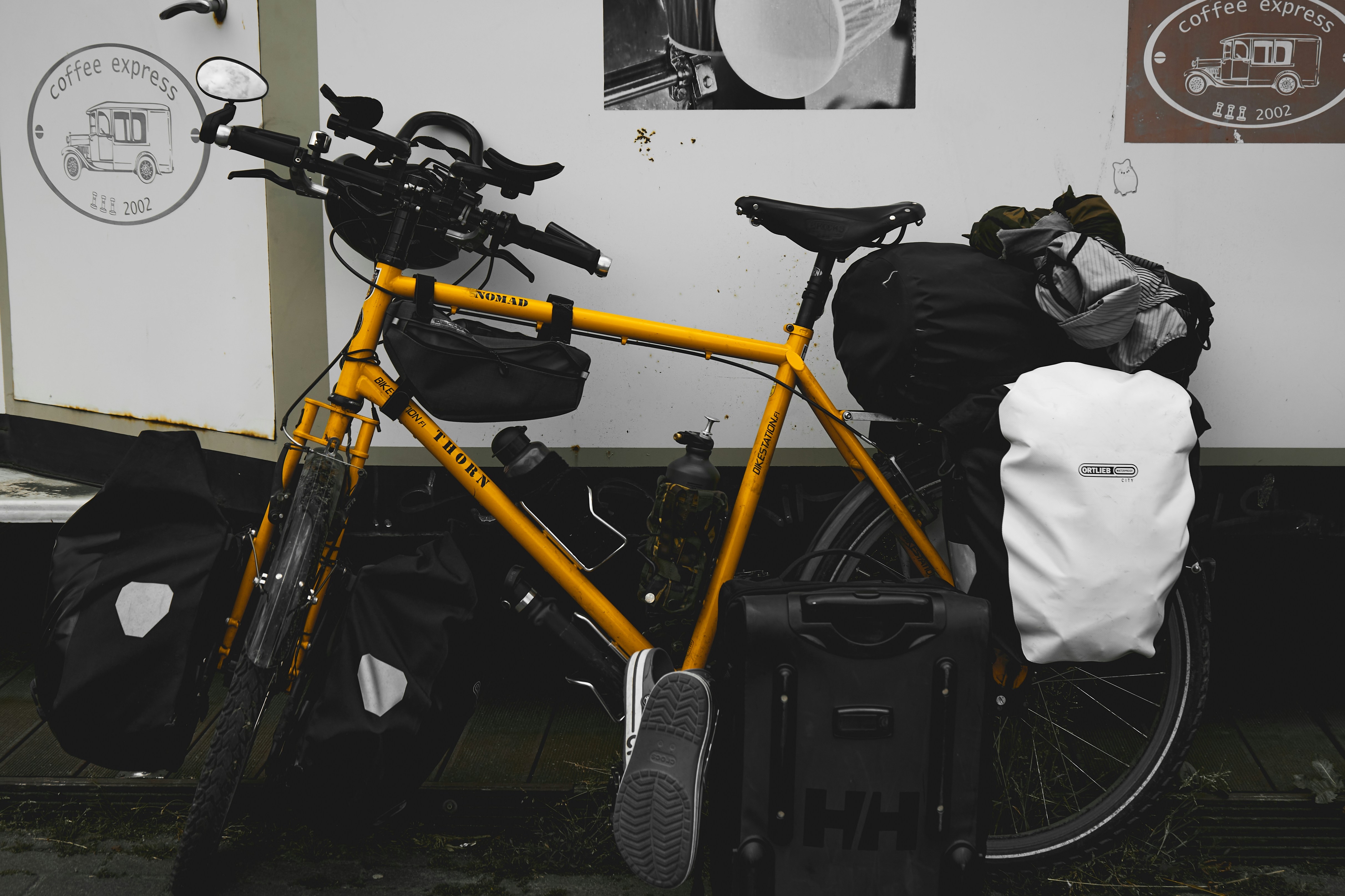 Yellow touring bicycle loaded with gear, parked next to a coffee shop, showcasing the spirit of adventure and exploration.