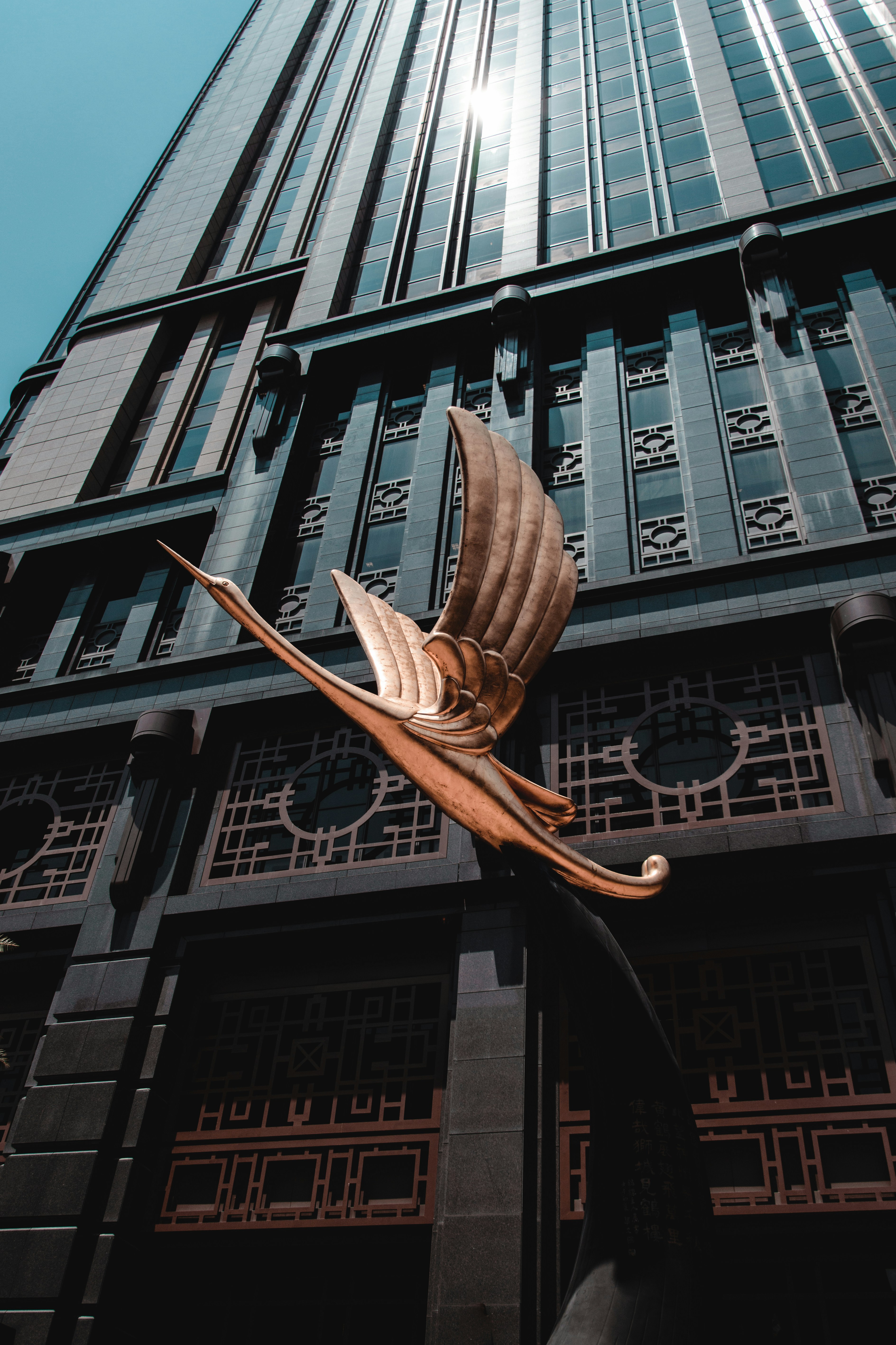Sculpture of a bird in flight, set against a towering modern building, showcasing a blend of art and architecture.