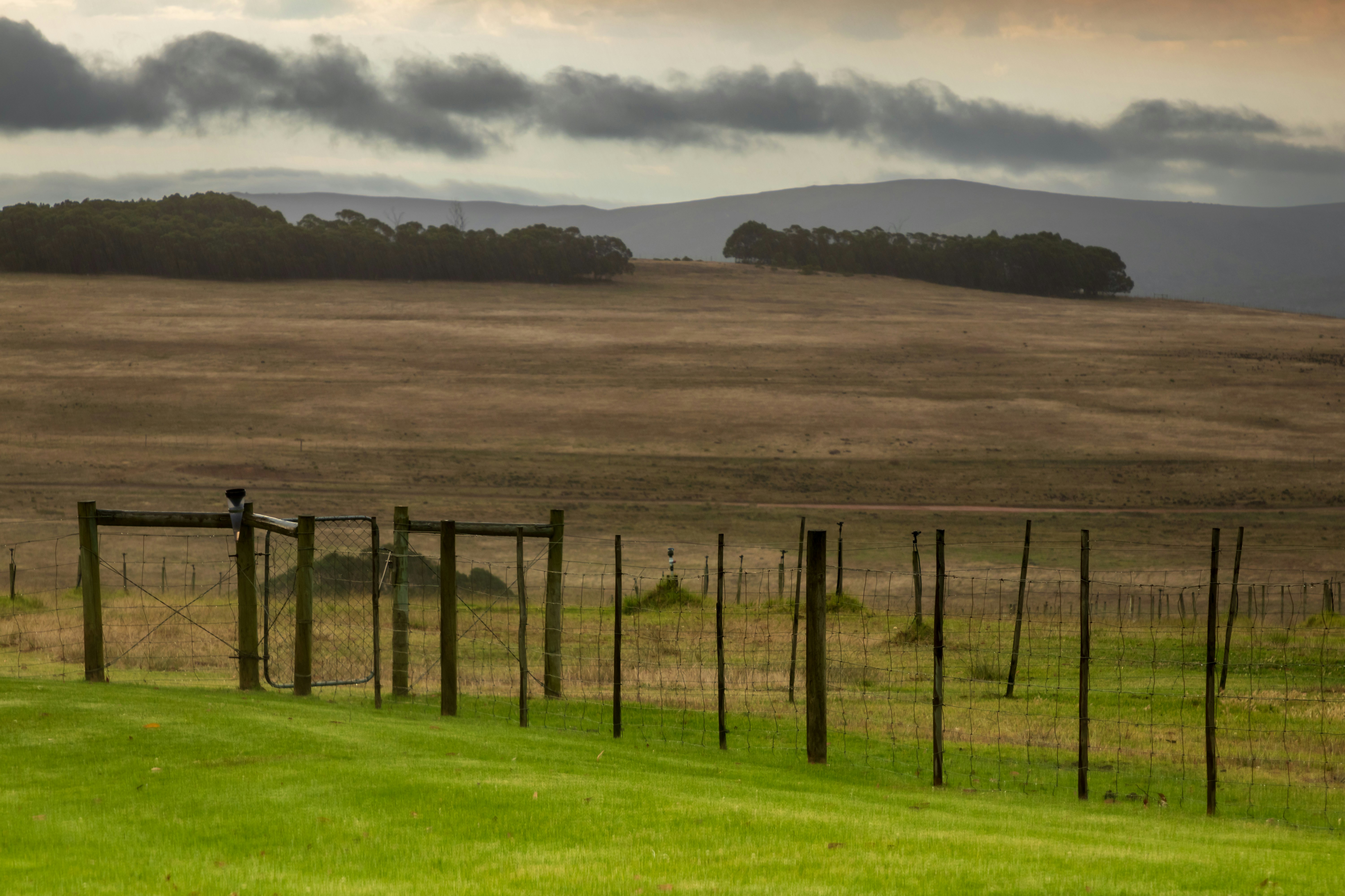 Sunset on a farm in the middle of nowhere with clouds in the sky and a farm fence in the foreground 