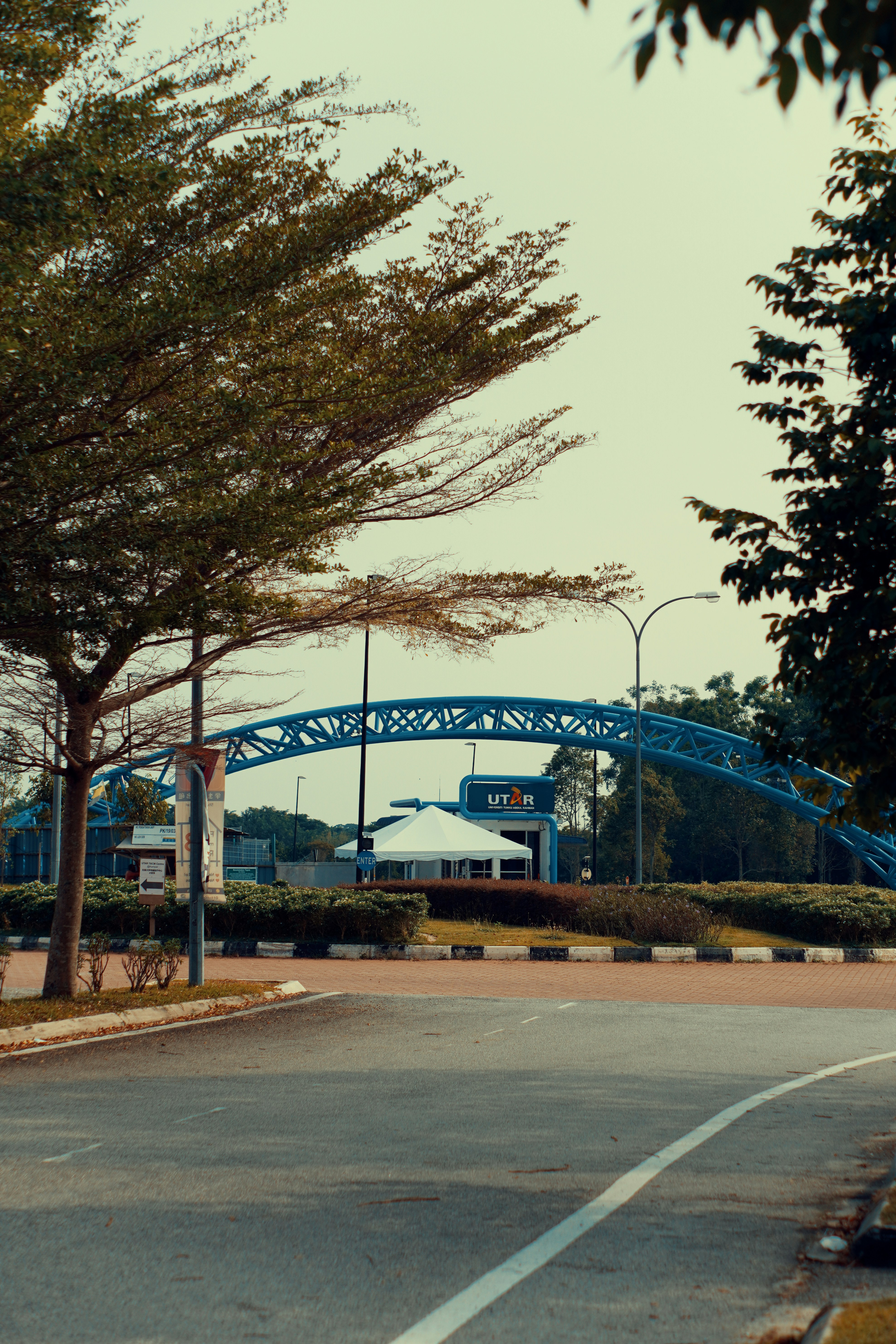A vibrant blue archway marks the entrance to a university campus, framed by lush trees and a winding road. The scene conveys a sense of academic pursuit and exploration.
