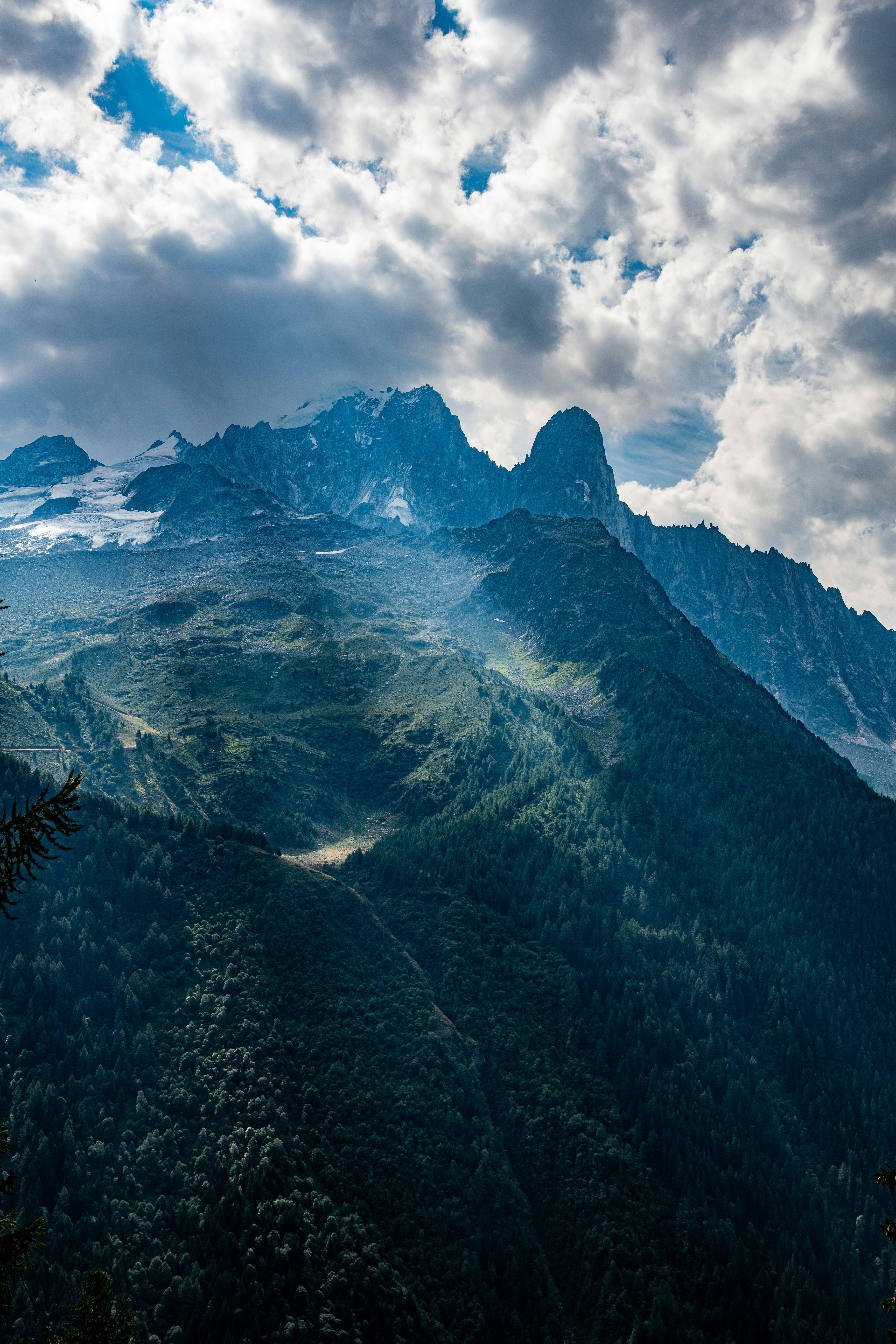 Majestic mountain range shrouded in mist, with lush greenery and dramatic clouds overhead.