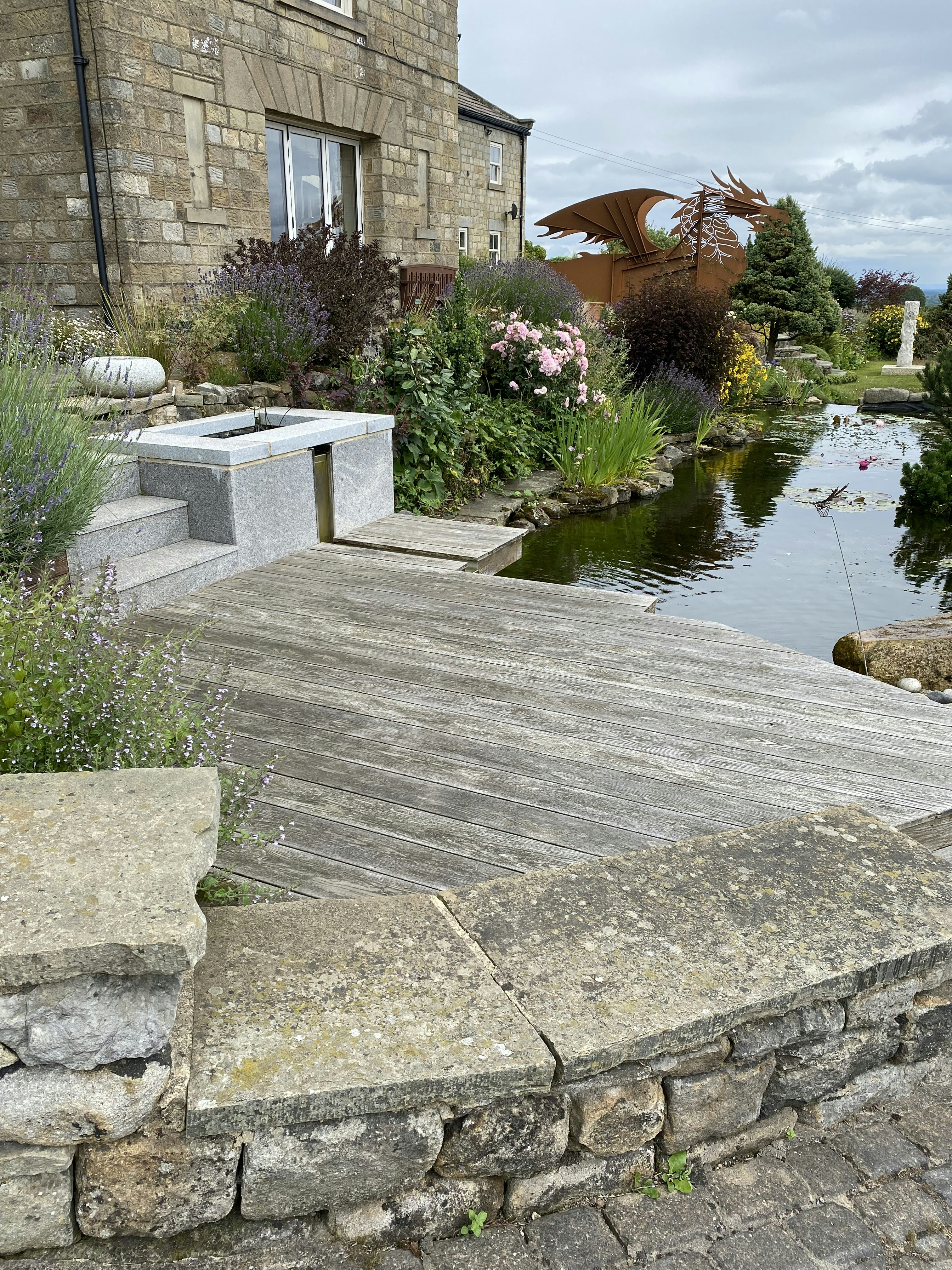 Stone pathway leading to a serene garden with lush greenery and a reflective pond.