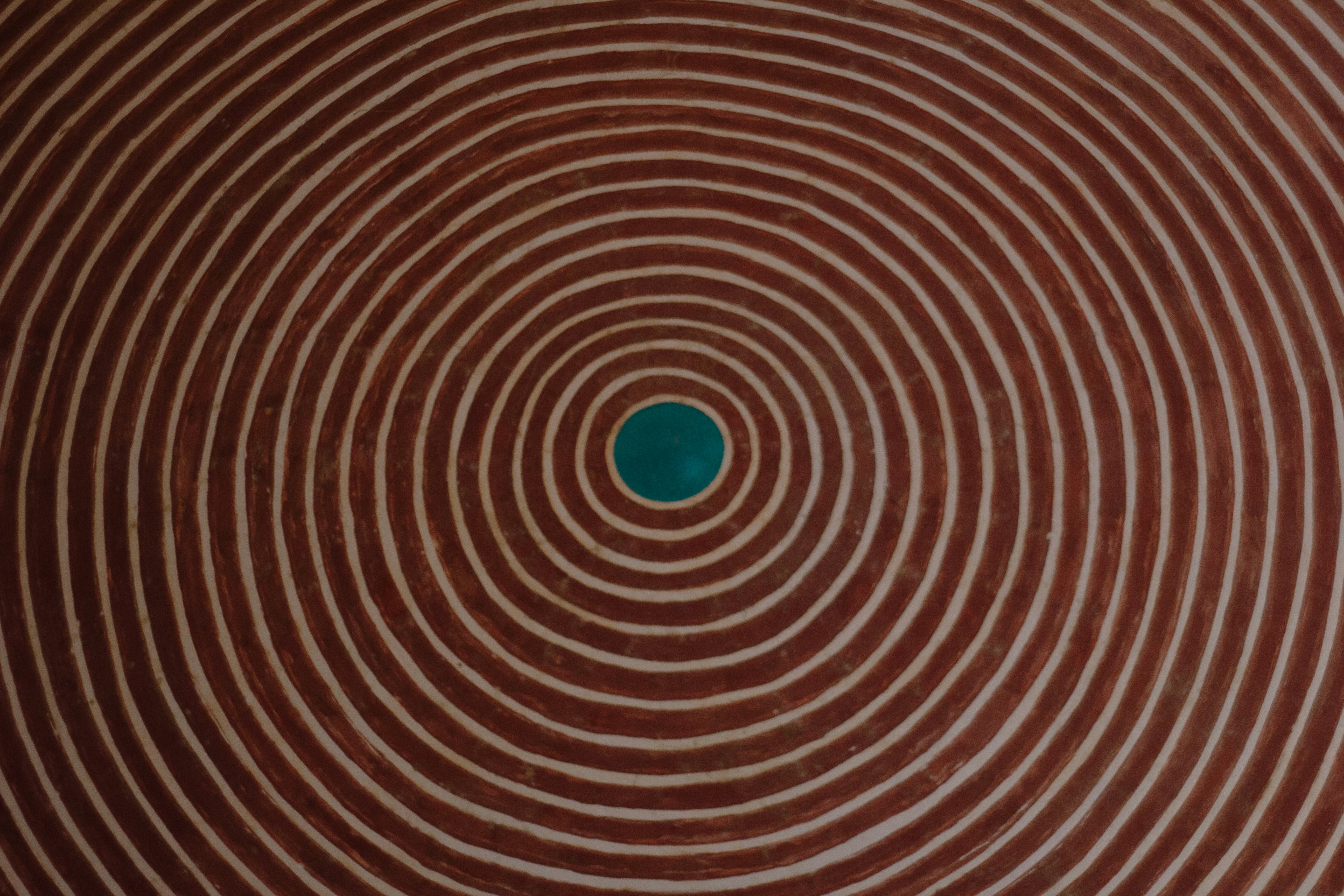 Concentric circles in earthy tones radiate from a vibrant turquoise center, creating a mesmerizing visual rhythm.