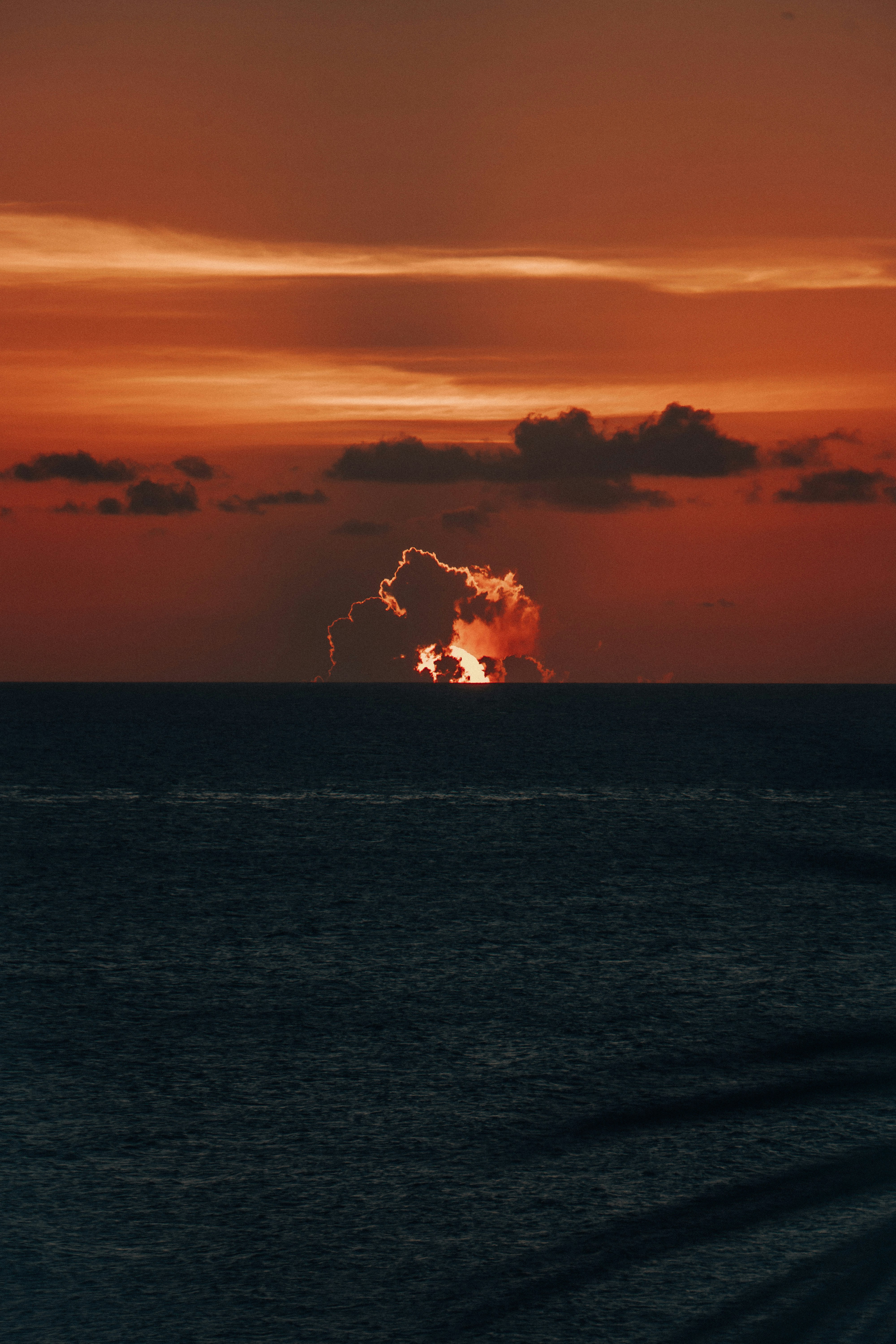 Sunset at the Horizon: A Cloud Burst Emerges Over Quiet Seas
