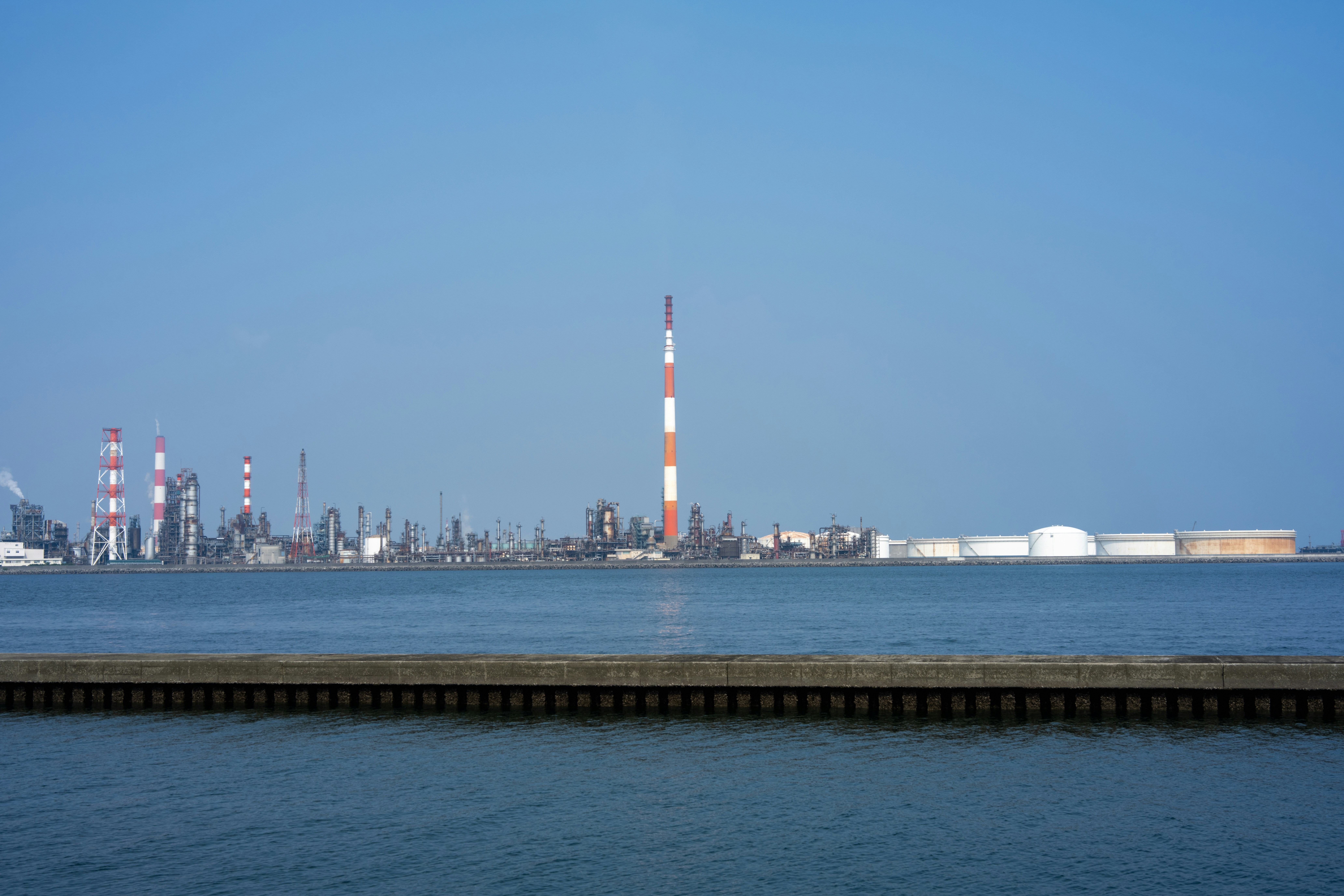 Industrial skyline across calm harbor under clear blue sky