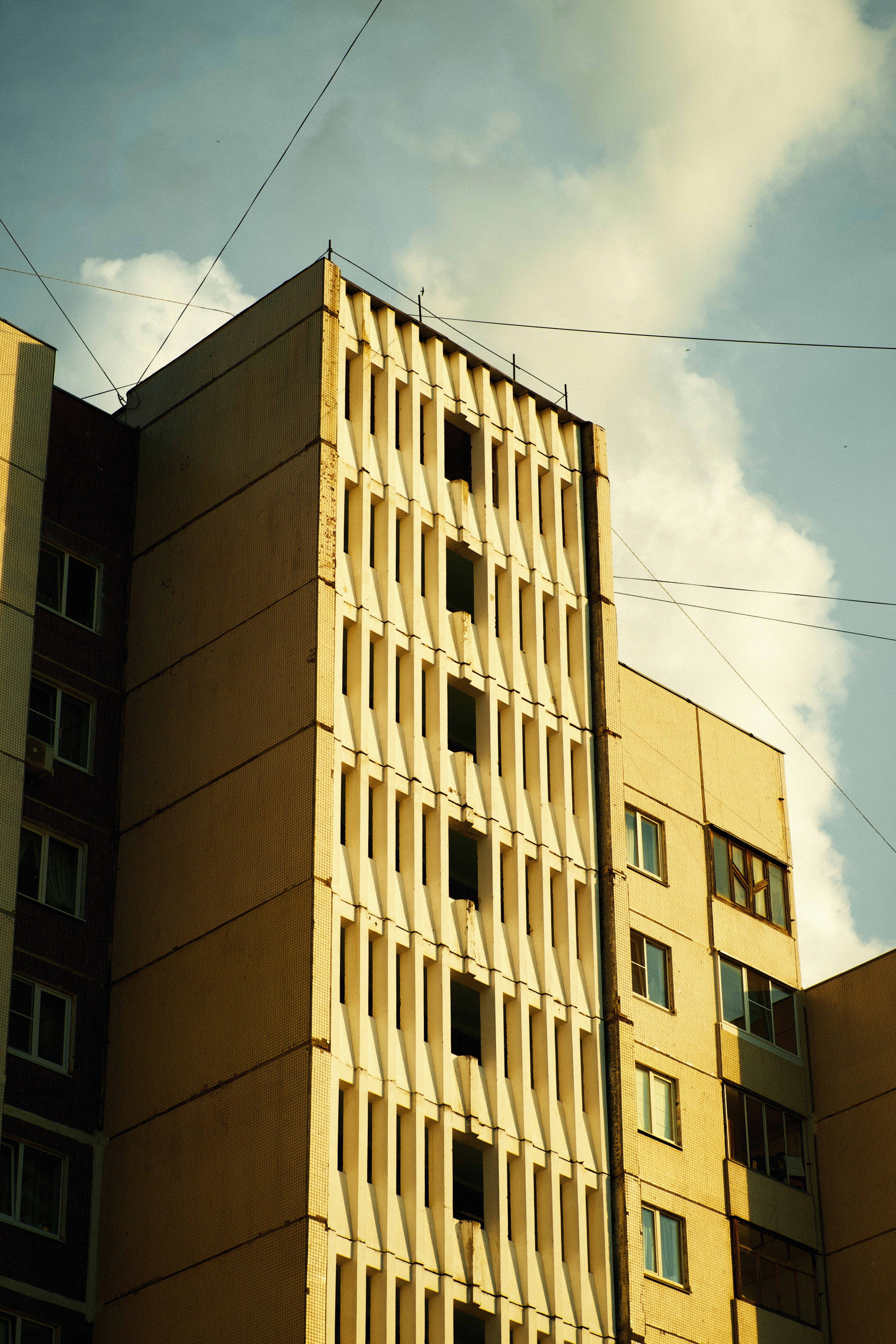 Architectural details of a high-rise building showcasing a unique geometric pattern and contrasting materials. Sunlight casts interesting shadows on the facade.