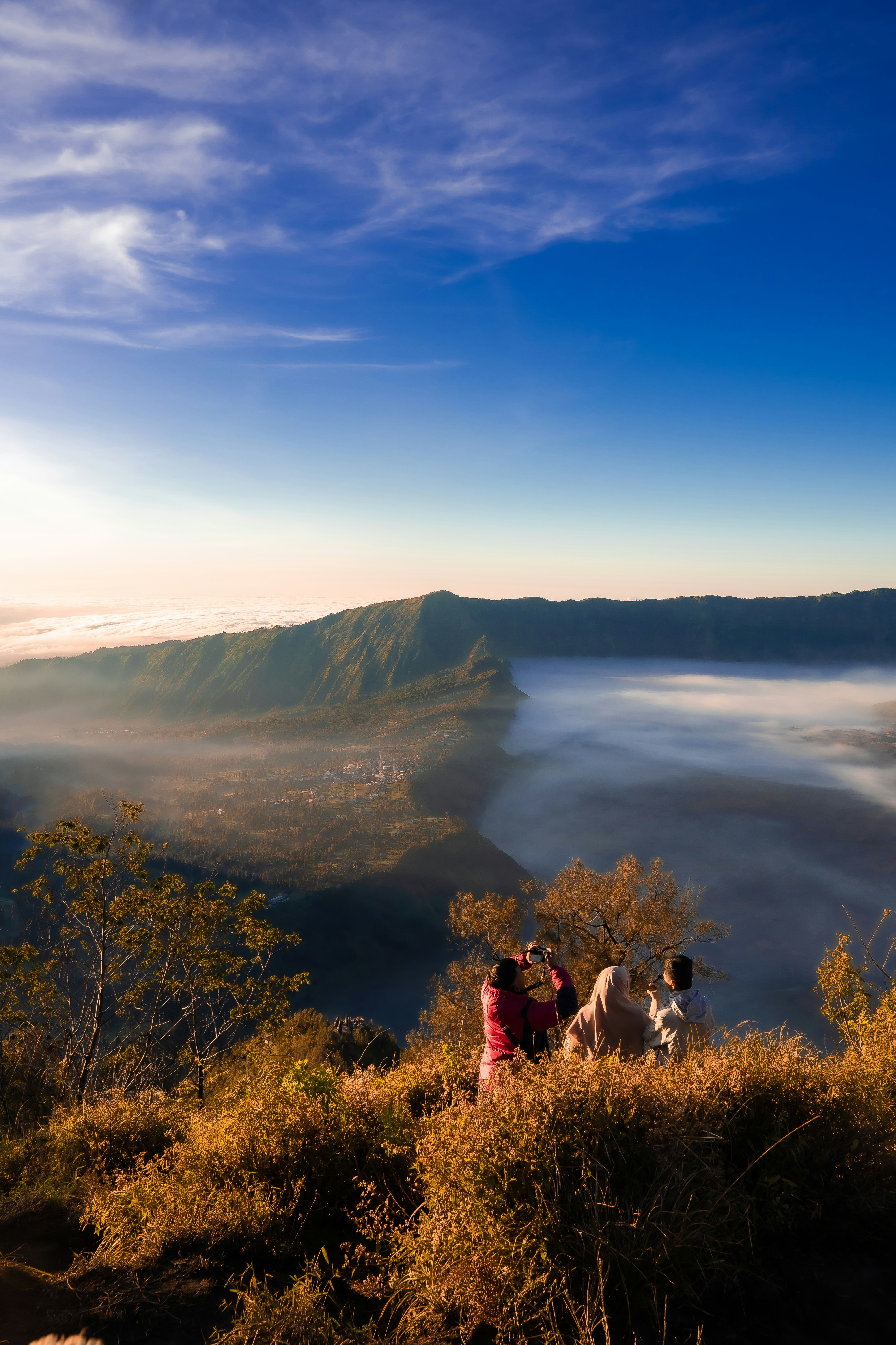 Group of people enjoying the view from a mountain peak as mist envelops the valley below during sunrise.