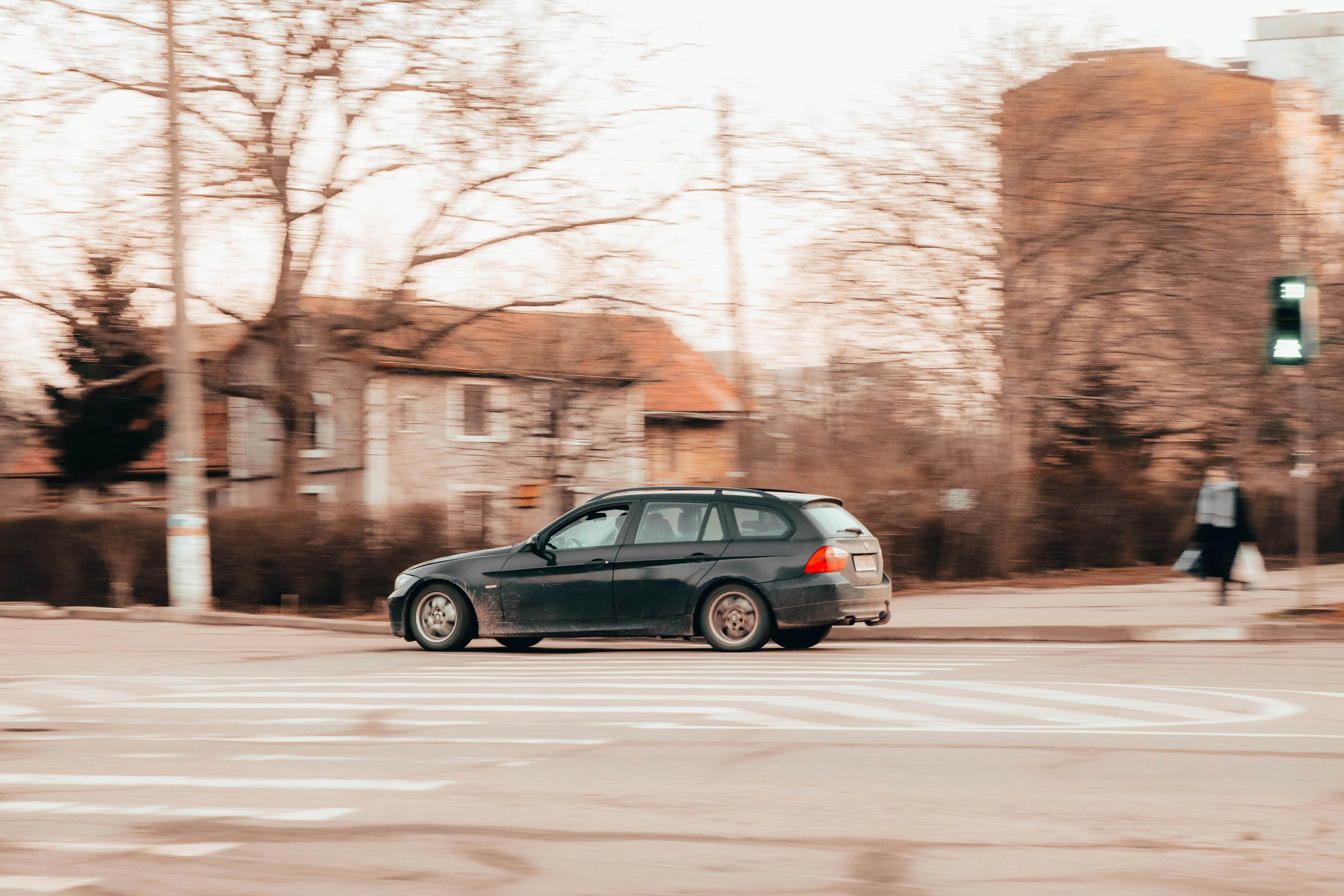 A black station wagon accelerates through an intersection, blurring the background in a dynamic display of urban life.