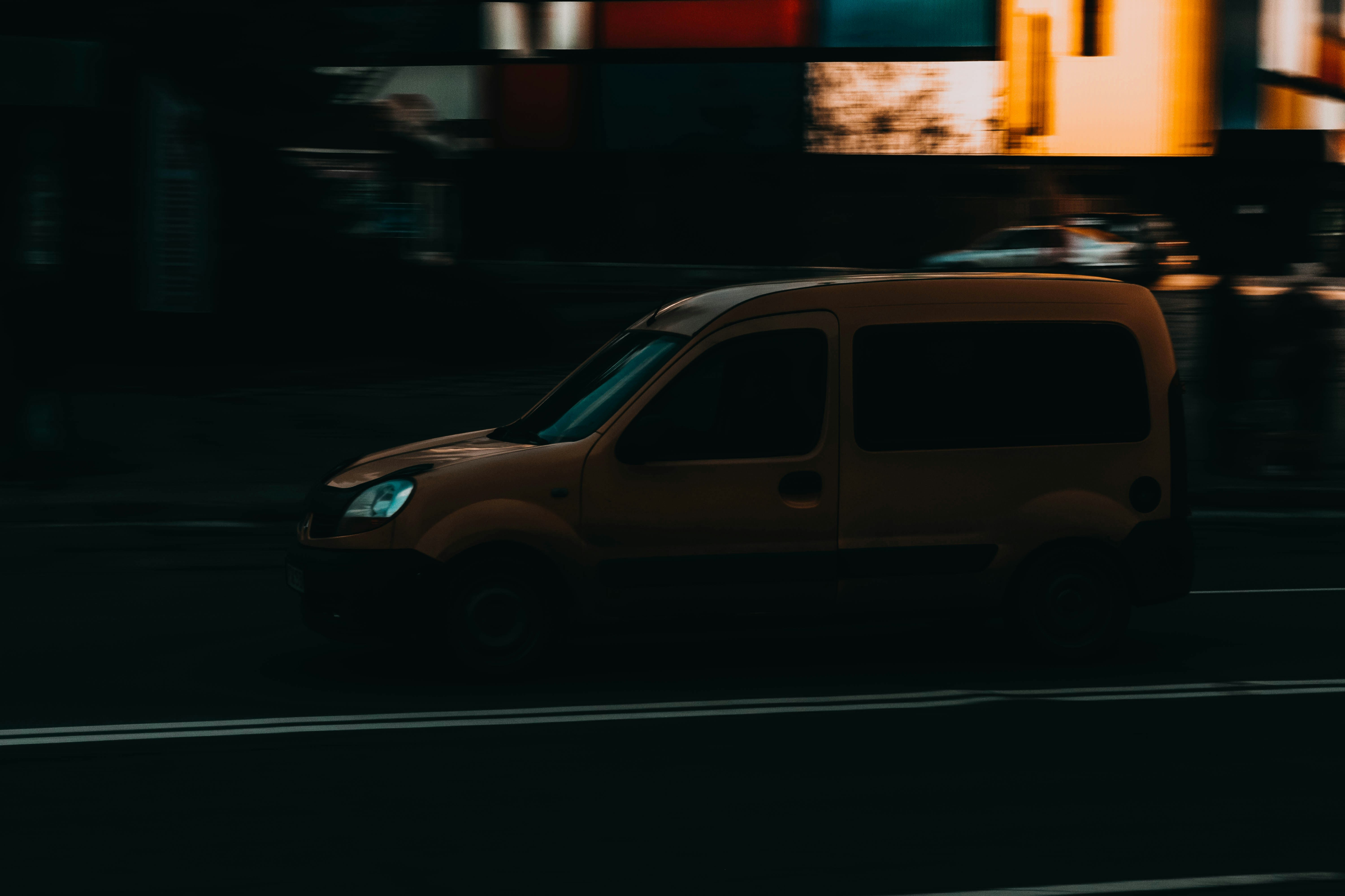 An orange van captured in motion against a backdrop of colorful urban structures, illustrating the hustle of city life.
