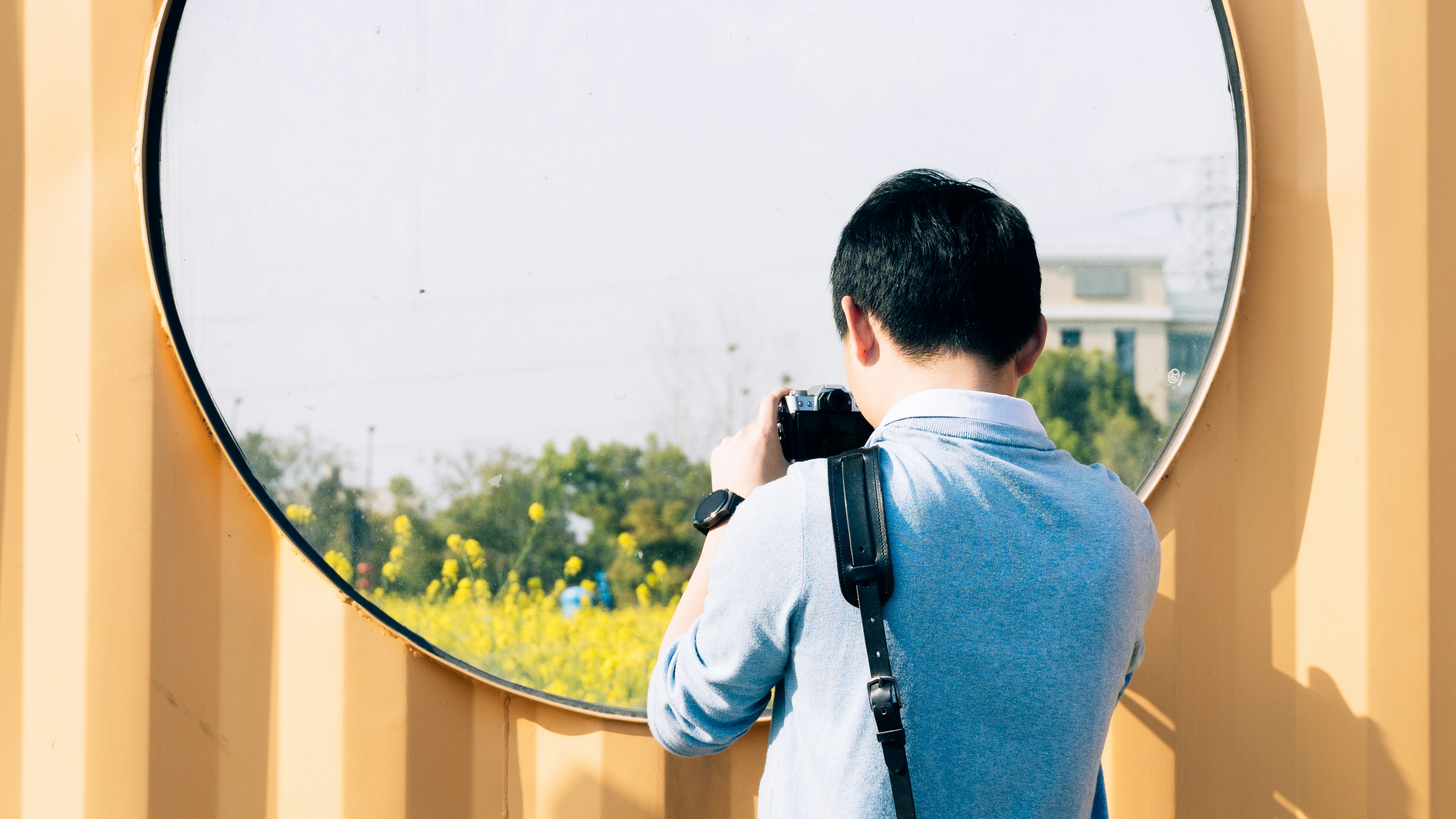 Round Portal, Focused Gaze: A Photographer Framed by Sunlit Yellow Architecture