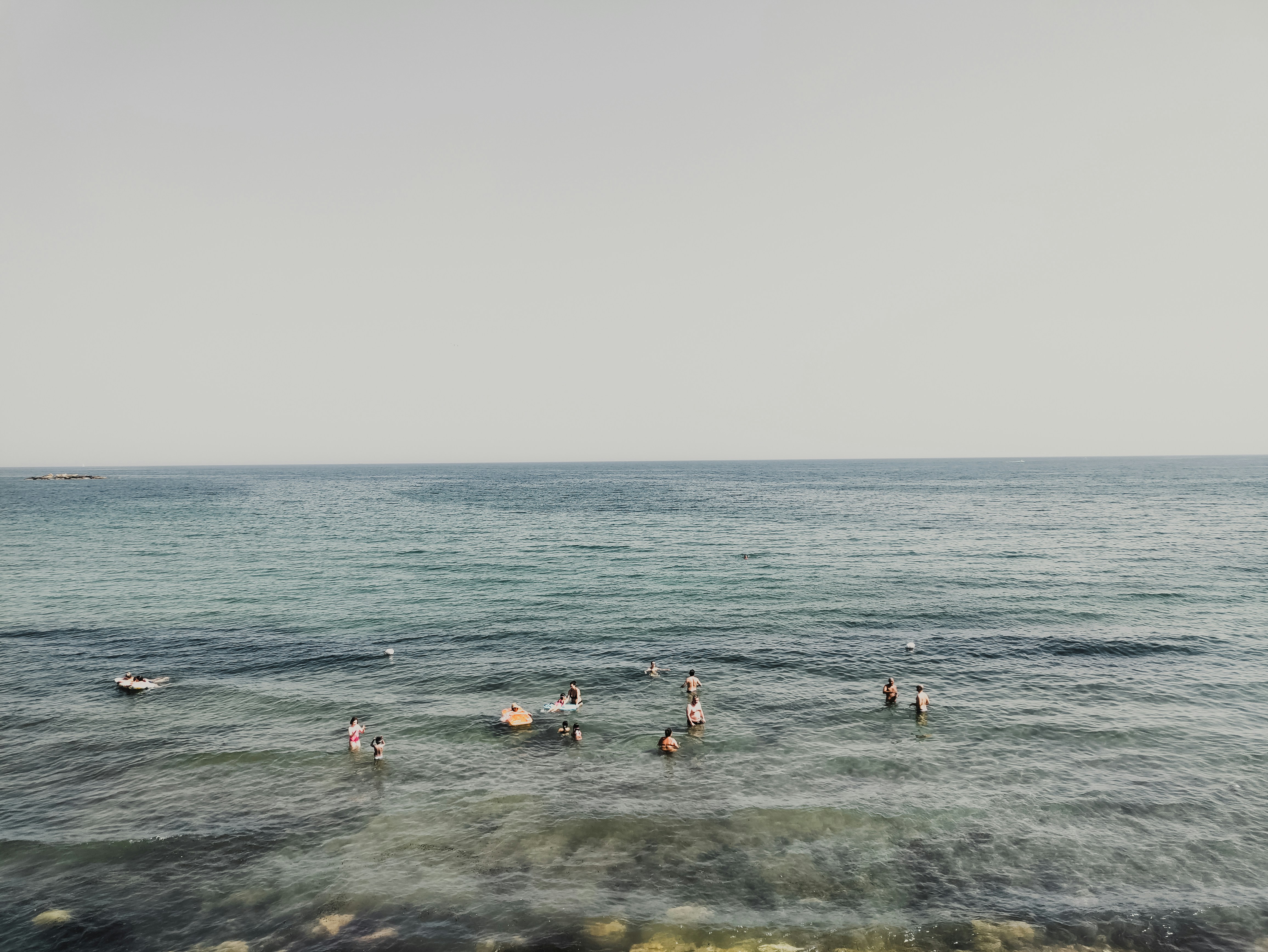 Calm sea with a group of birds wading near the shore under a clear sky.
