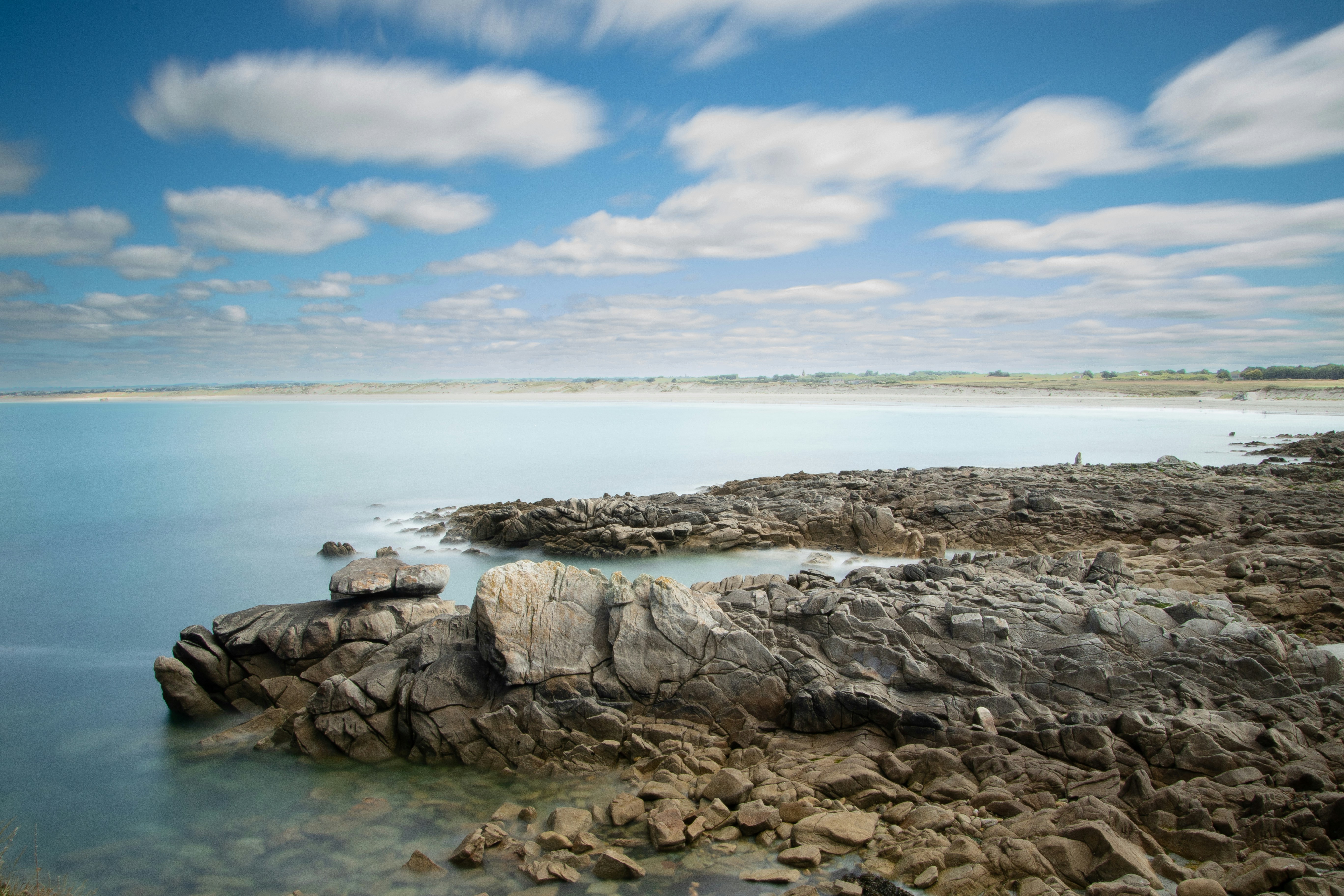Rocky shoreline at calm turquoise lagoon under a sky of drifting clouds