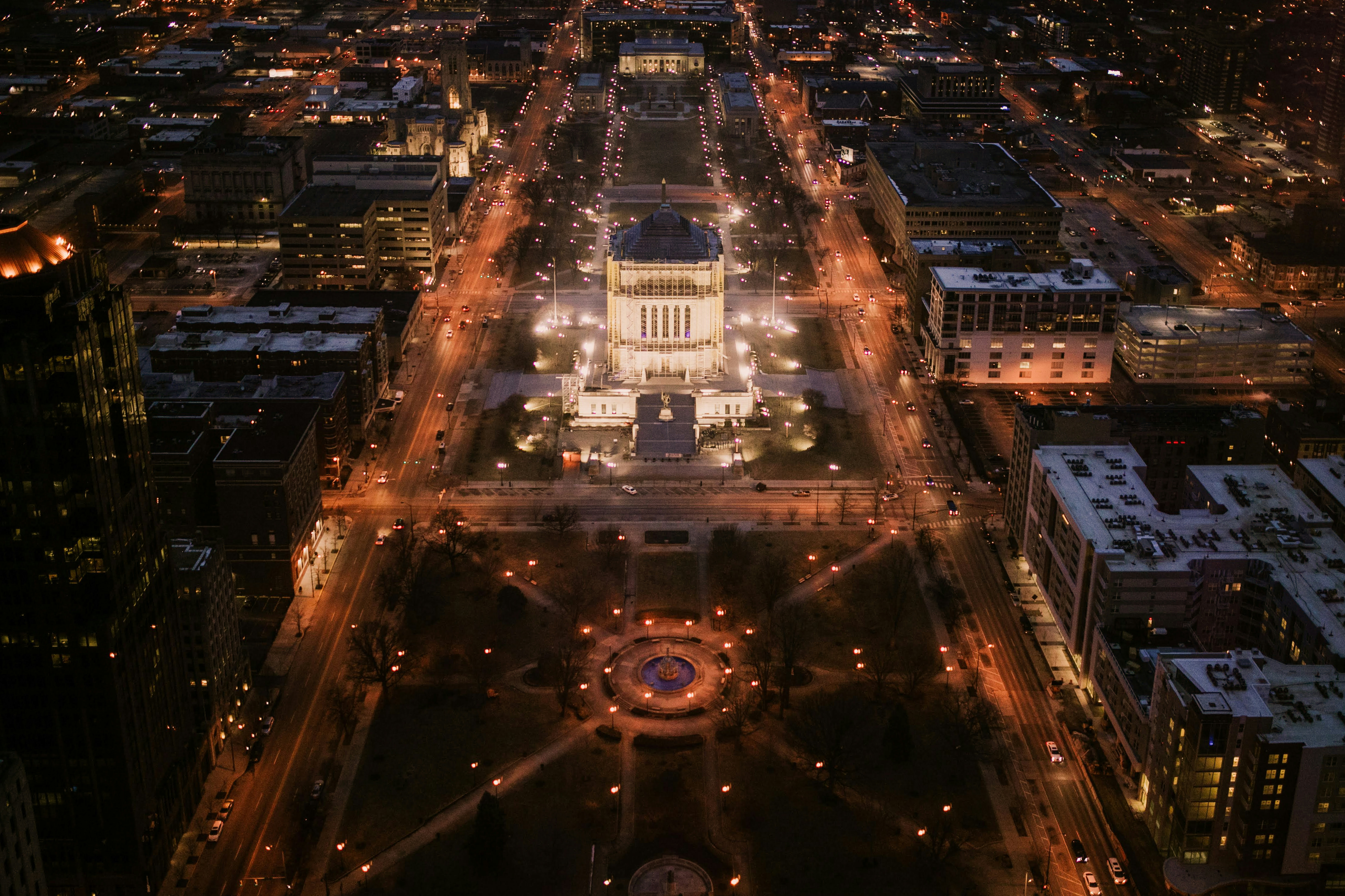 Aerial view of a cityscape illuminated at night, showcasing the grandeur of a central building surrounded by bustling streets and glowing lights.