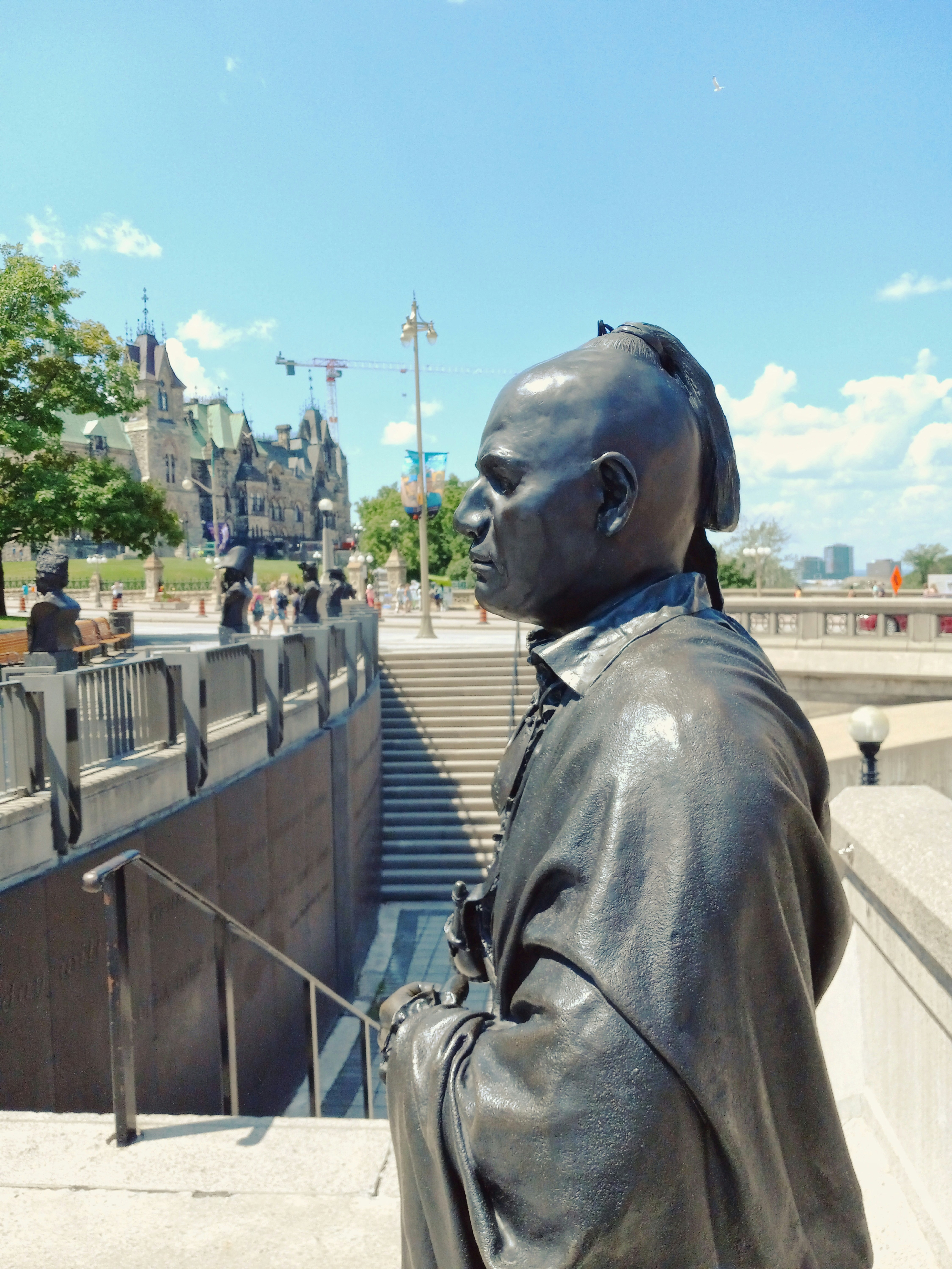 Bronze statue of a historical figure overlooking a staircase, with architectural details and greenery in the background.