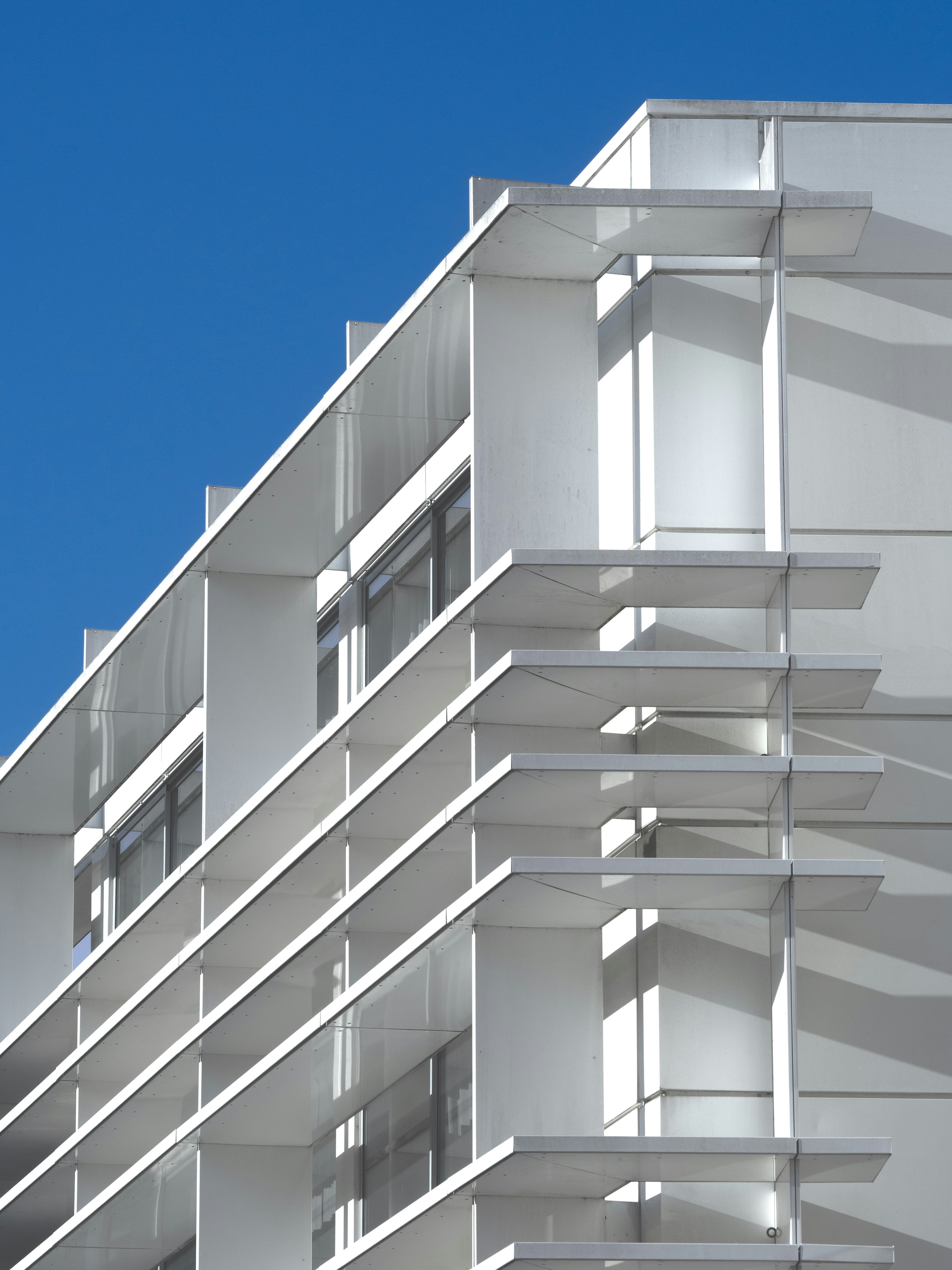 White architectural facade with geometric lines set against a clear blue sky.