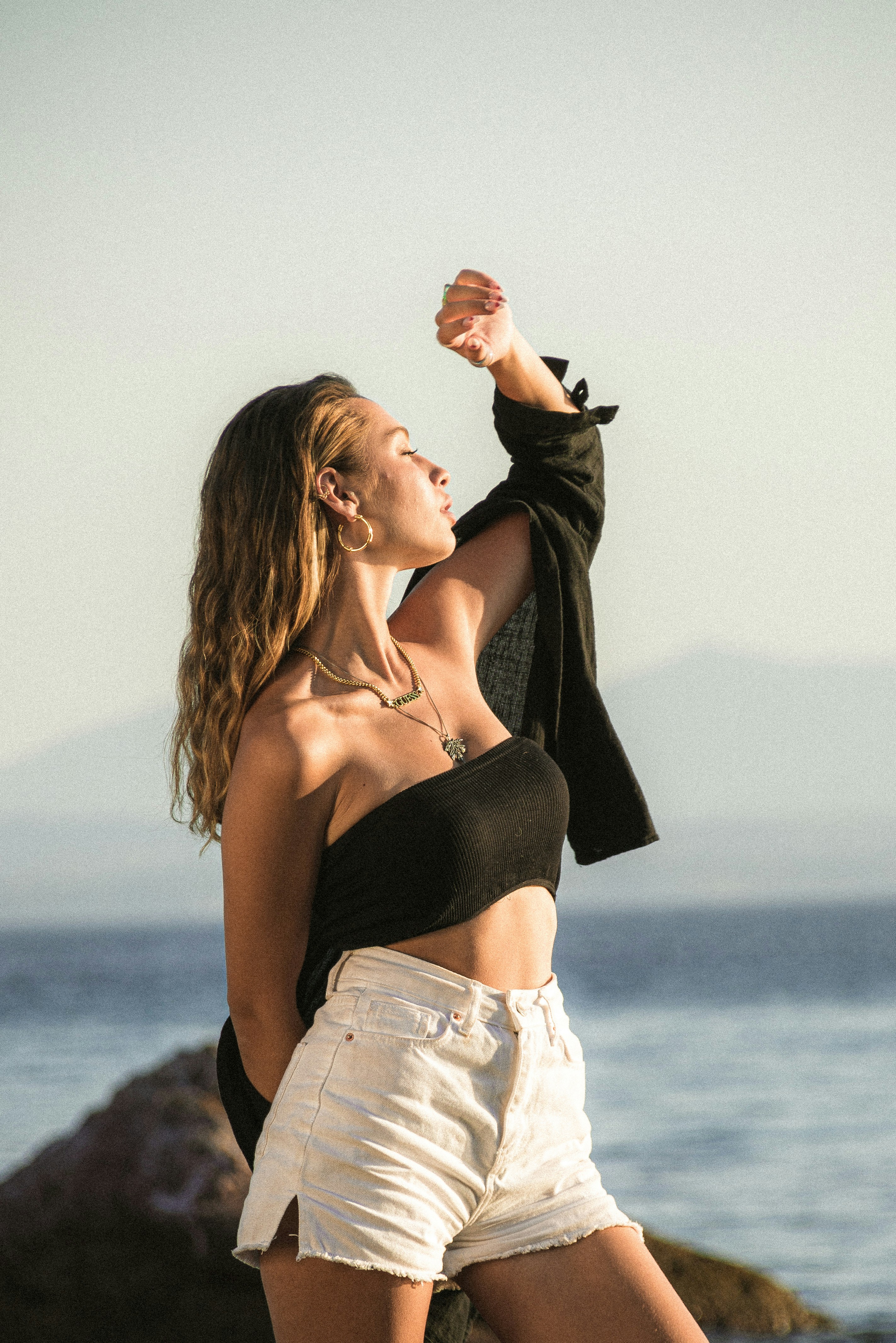 Woman striking a pose against a tranquil seascape, capturing the essence of summer freedom. The soft light enhances the serene atmosphere.