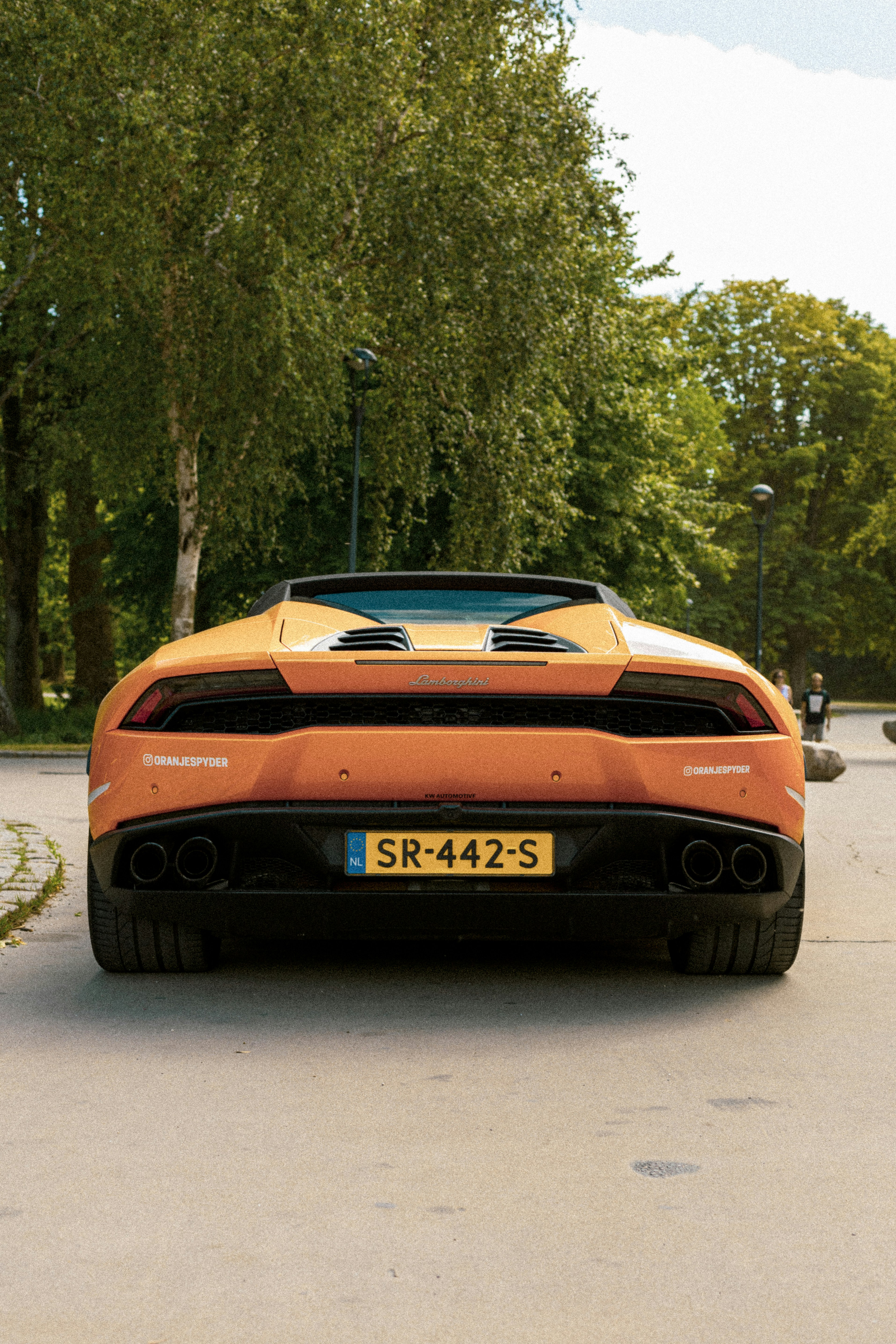 Rear-View Power in a Parkside Glow: Orange Huracán Resting by the Trees
