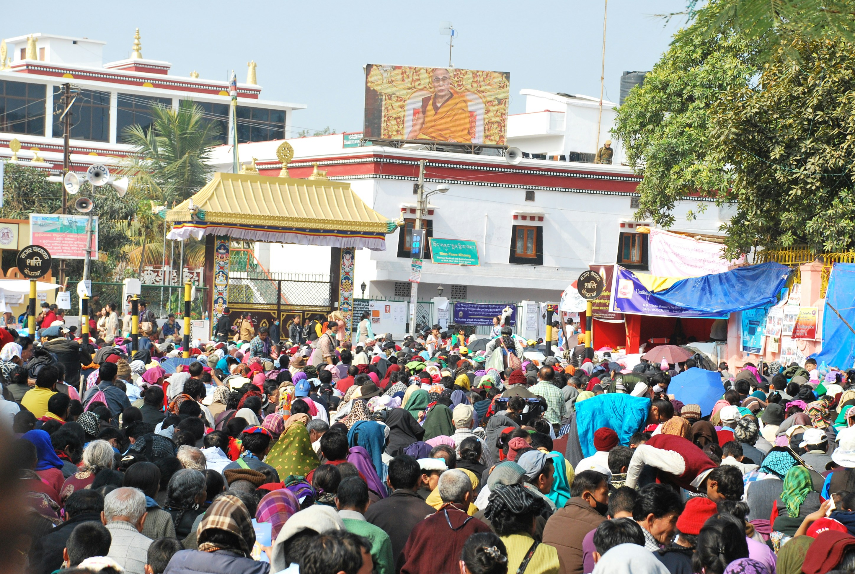 Crowd of people gathered near a golden-roofed pagoda under a clear sky.