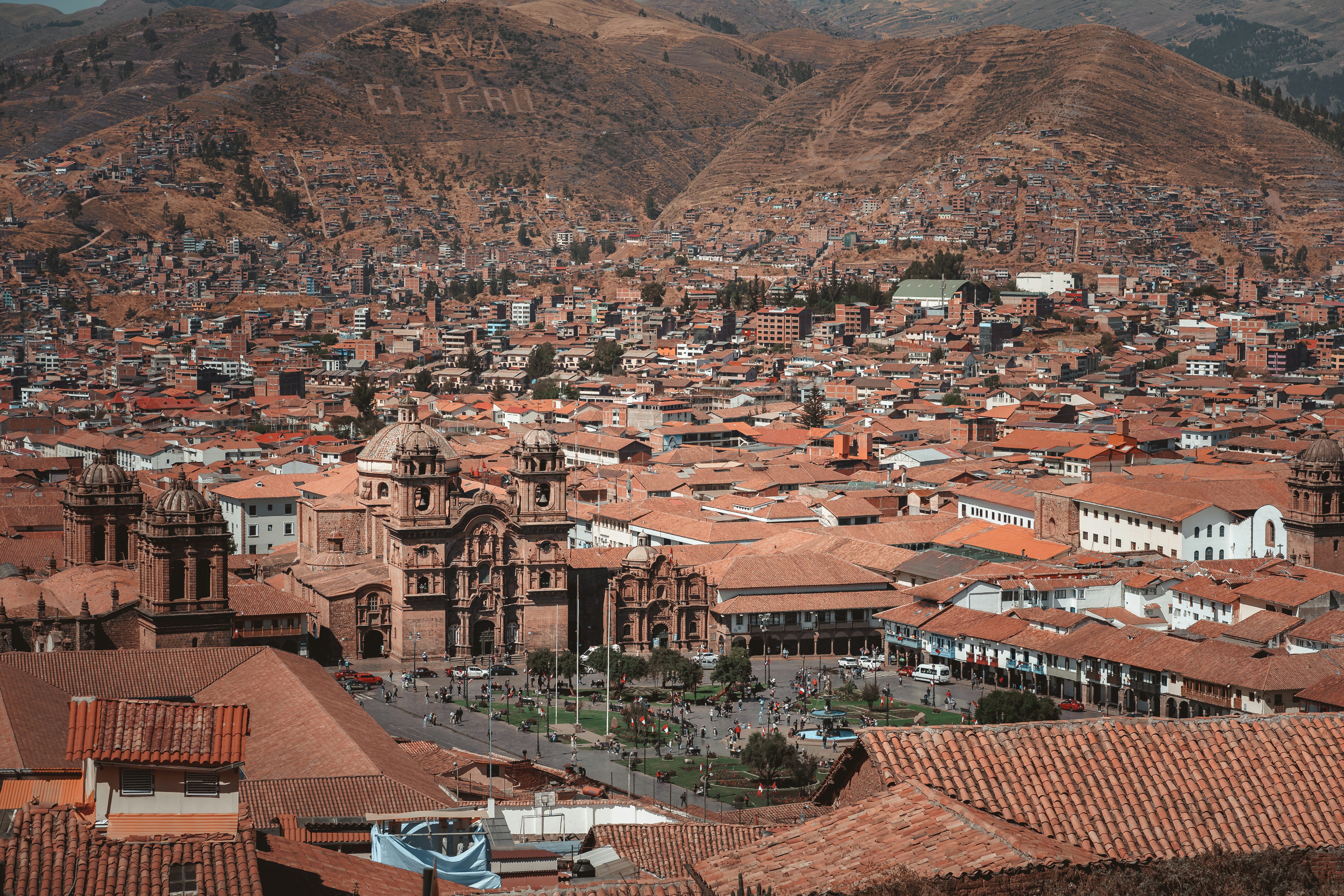 A panoramic view of Cusco, showcasing its terracotta rooftops and historic architecture, with the Andes mountains in the background.