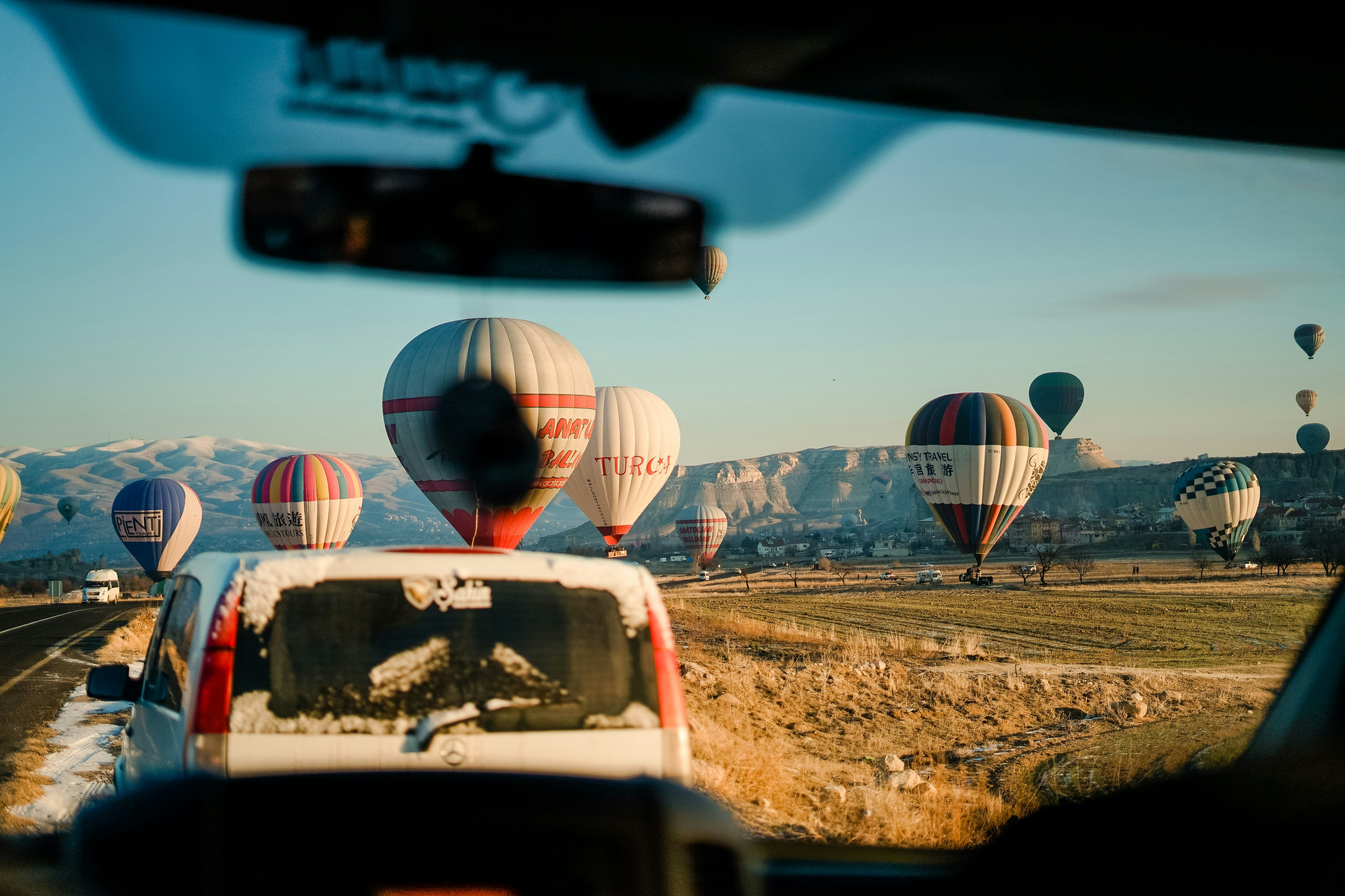 Colorful hot air balloons floating over a scenic landscape, viewed through a vehicle's windshield. The scene captures the essence of adventure and tranquility.