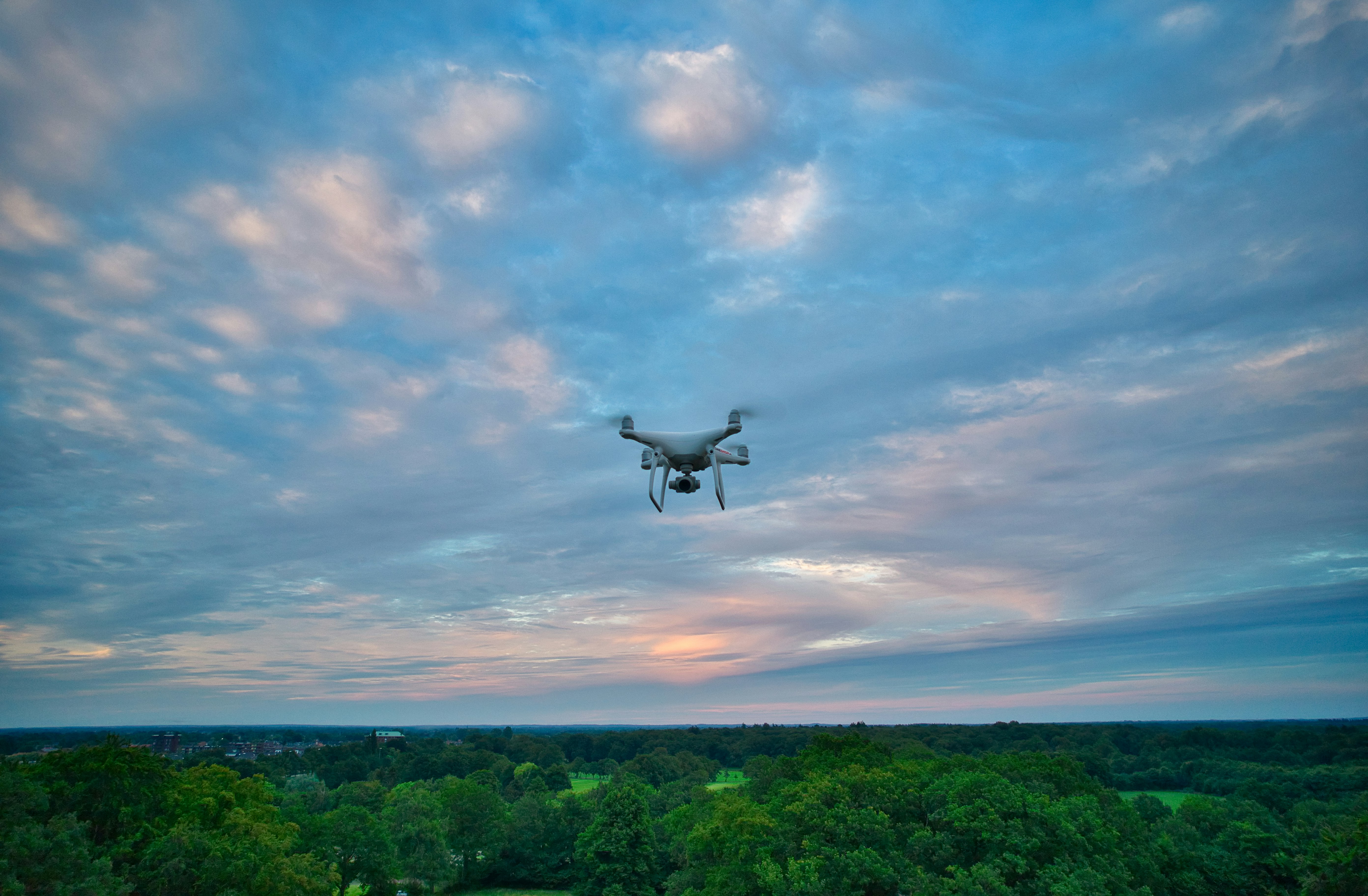 Aerial view of a drone hovering over a lush green landscape under a dramatic, cloud-filled sky at sunset.
