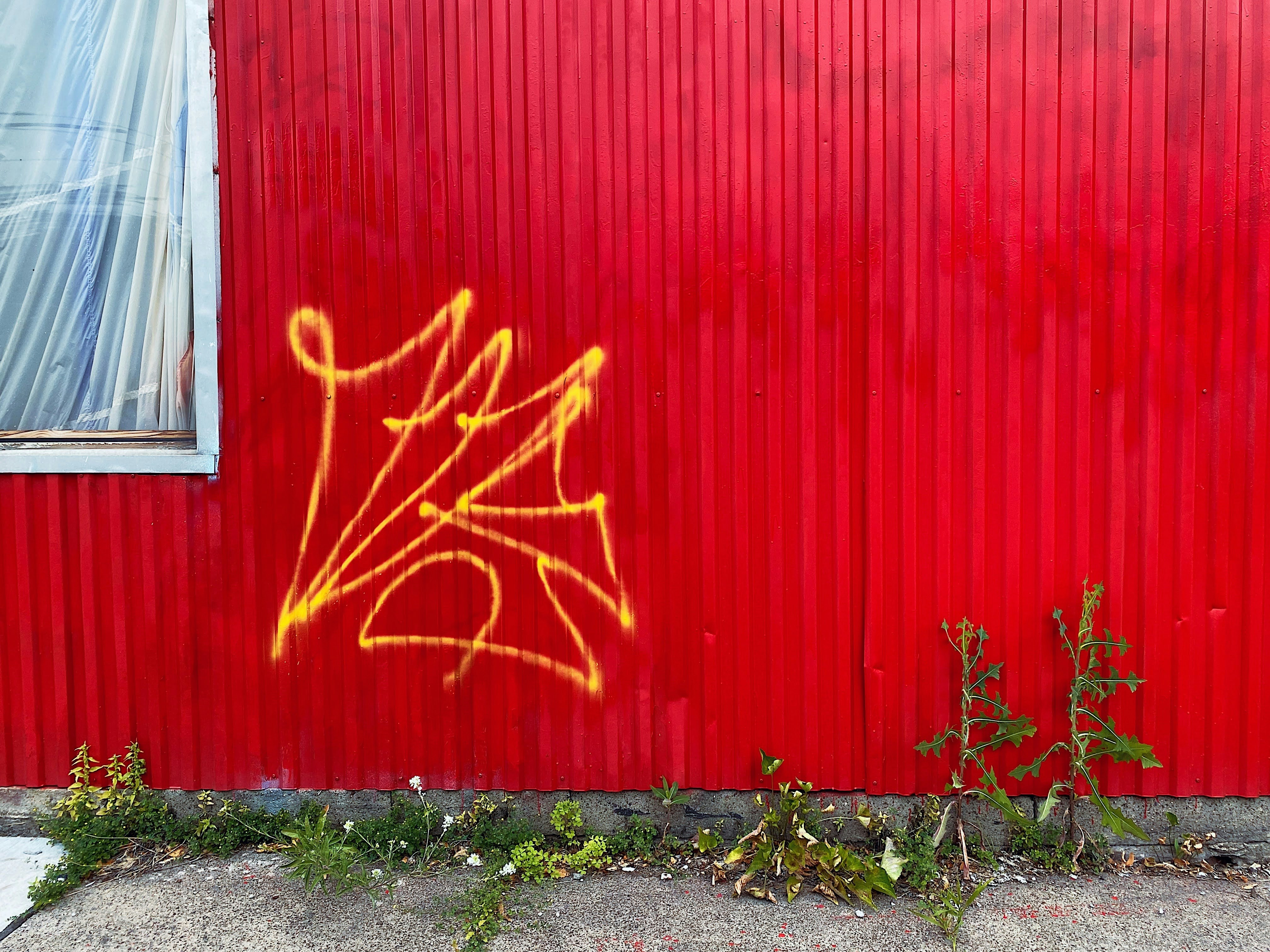 Amber Graffiti Tag on a Crimson Corrugated Wall Under a Narrow Window