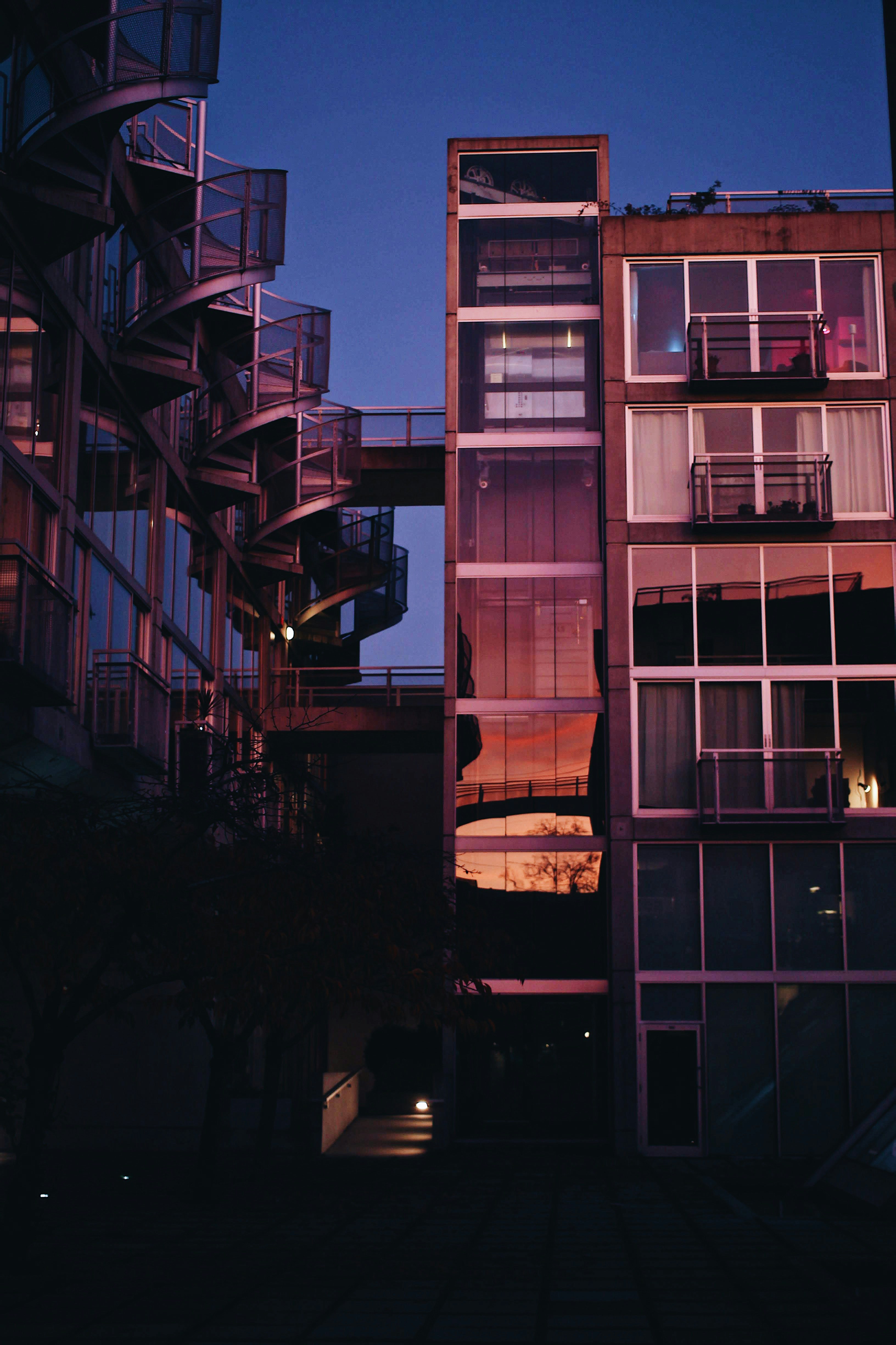 Modern architectural structure reflecting twilight hues, showcasing a blend of glass and steel. The spiral staircase adds a dynamic element to the composition.