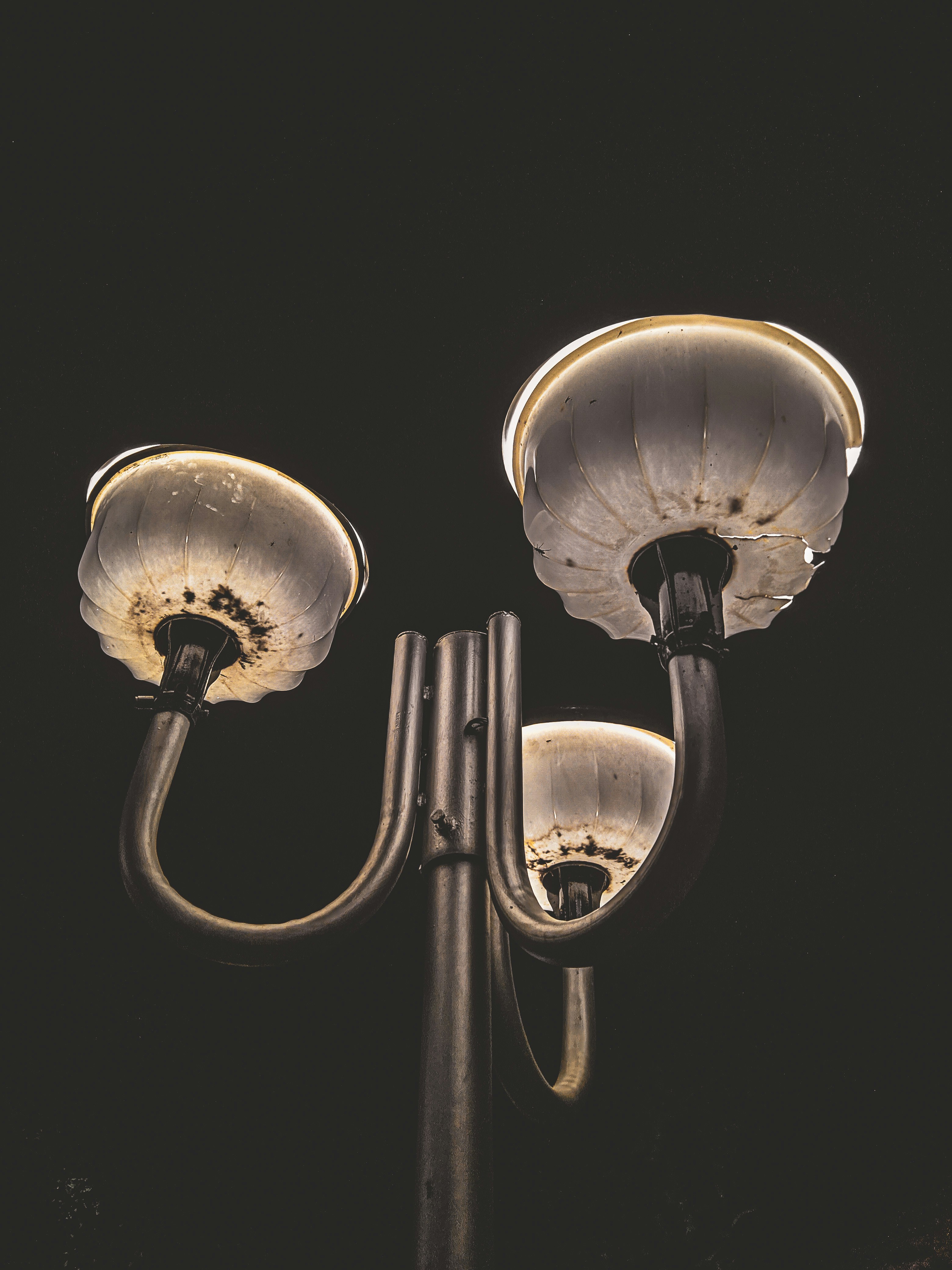 Low-angle photograph of a three-arm streetlamp with frosted glass globes glowing warmly against a dark night sky.