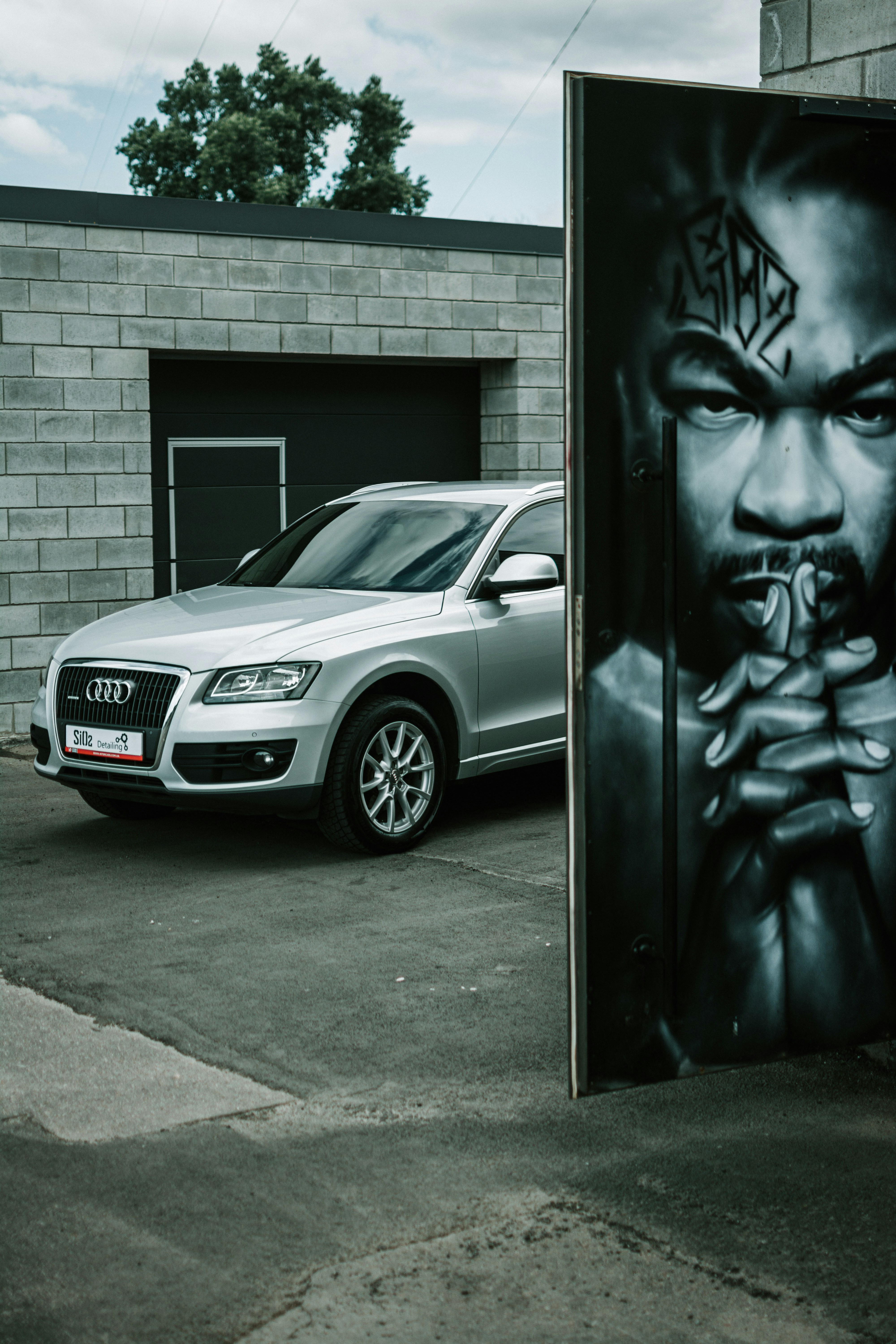 Street Quiet: Silver Audi at the Edge of a Graffiti Portrait