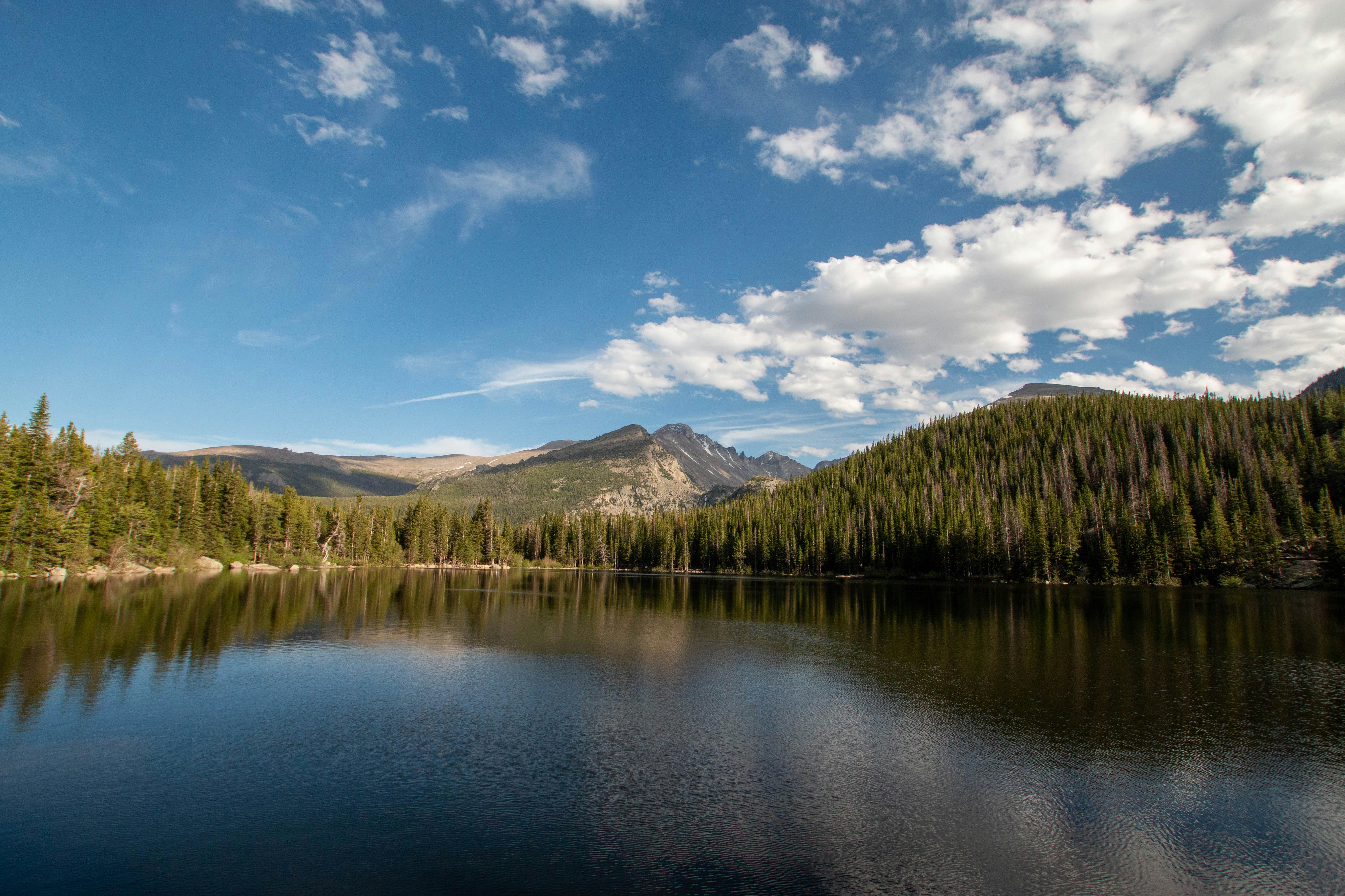 A serene mountain lake surrounded by lush forests and towering peaks under a clear blue sky. The still water reflects the vibrant landscape beautifully.