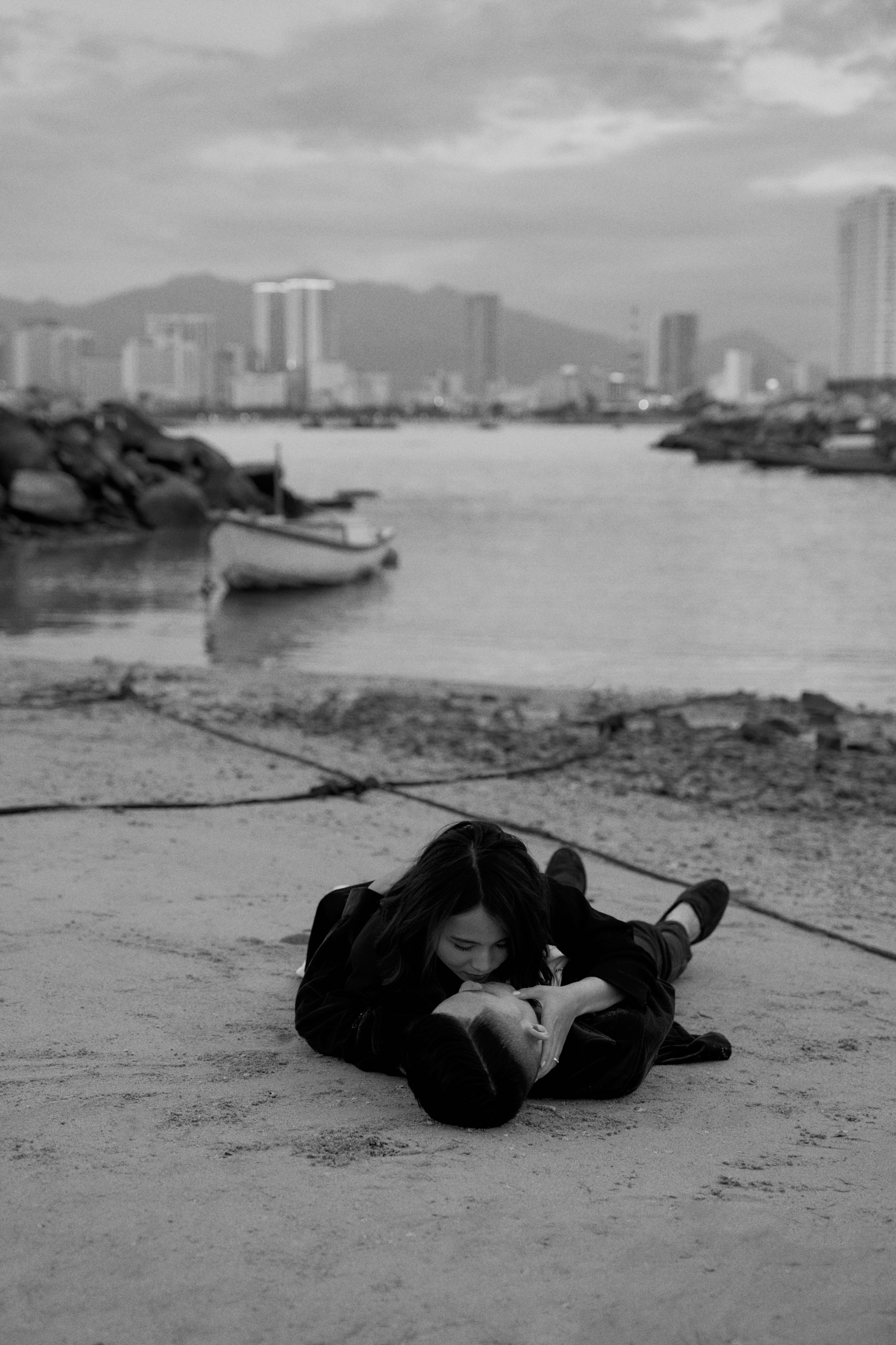 Person lying on a dock near water with cityscape in the background.