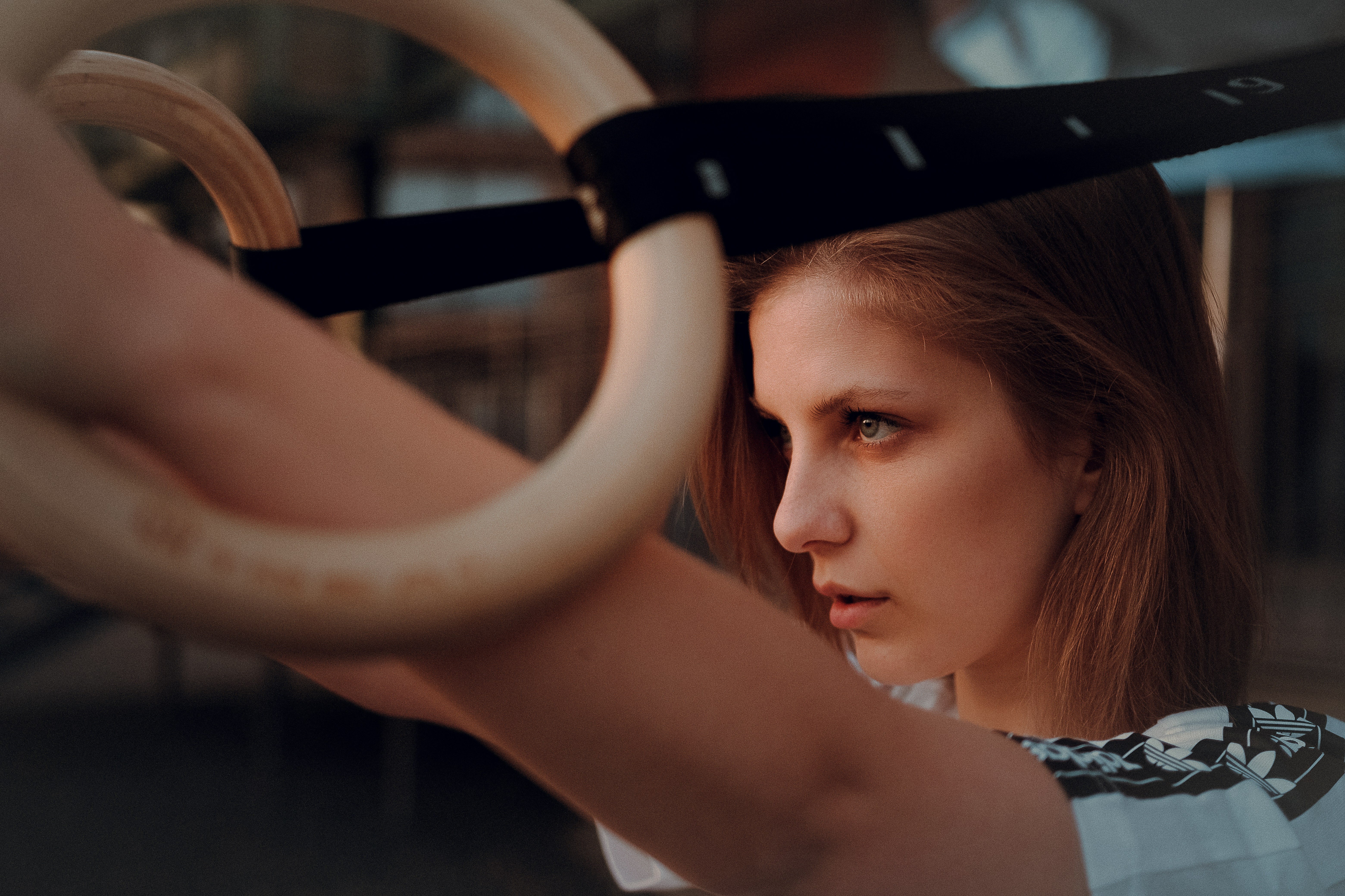 A young woman intensely focused on gymnastic rings, showcasing her determination and strength. The background hints at a training environment.