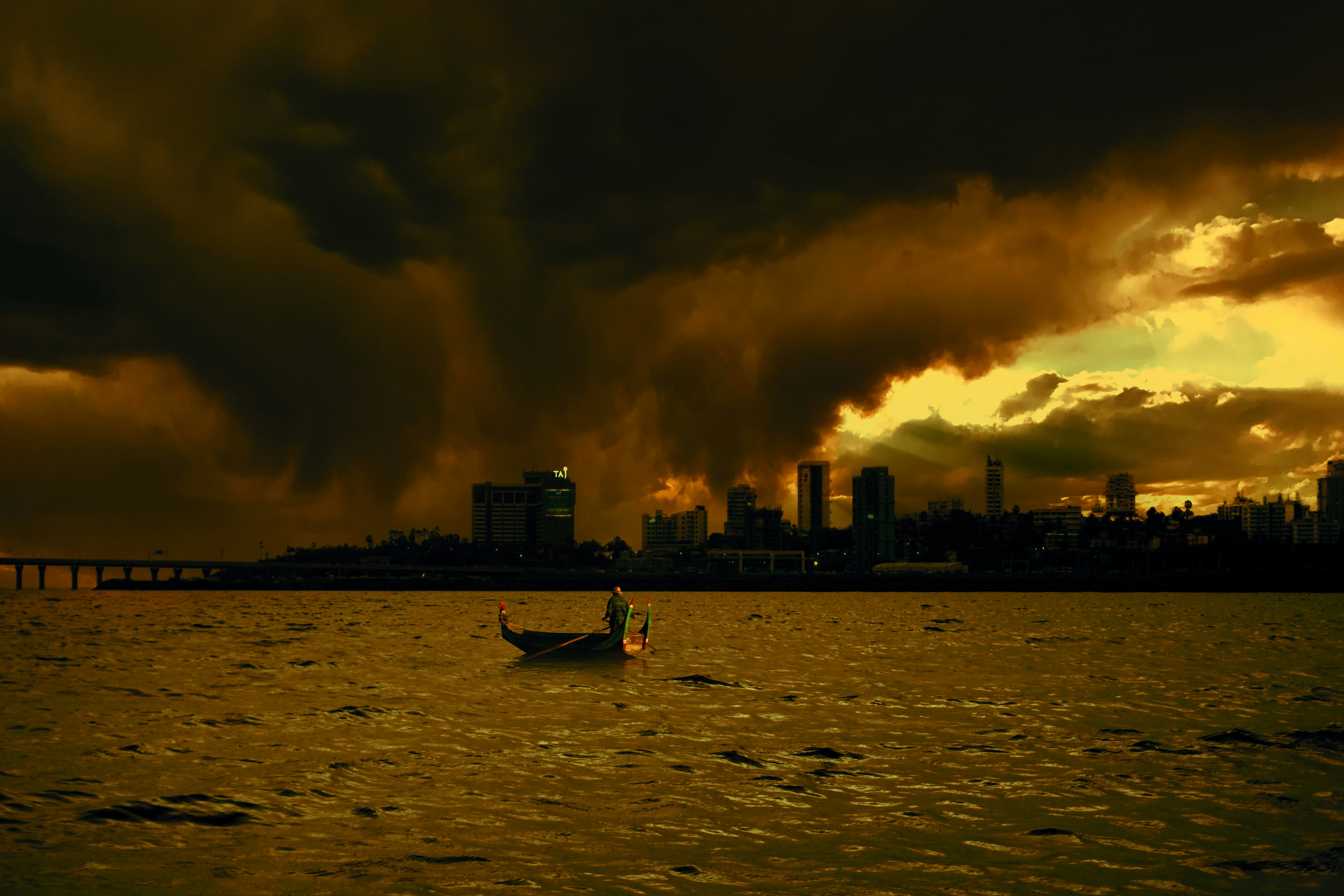 A lone fisherman navigates a shimmering sea under ominous storm clouds, with a city skyline silhouetted in the background.