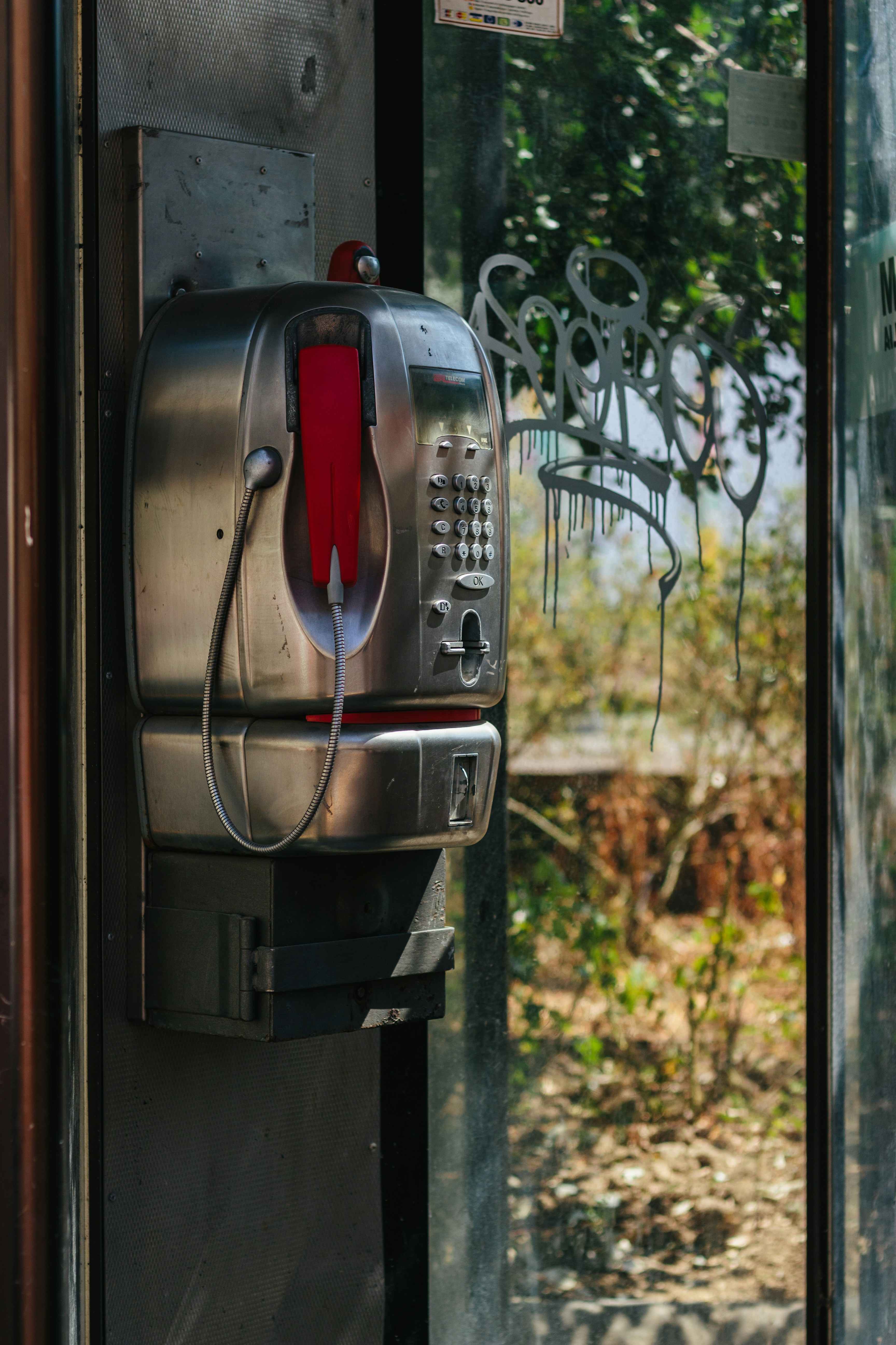 Red Handset Echo at a Weathered Payphone Amid Graffiti Glass