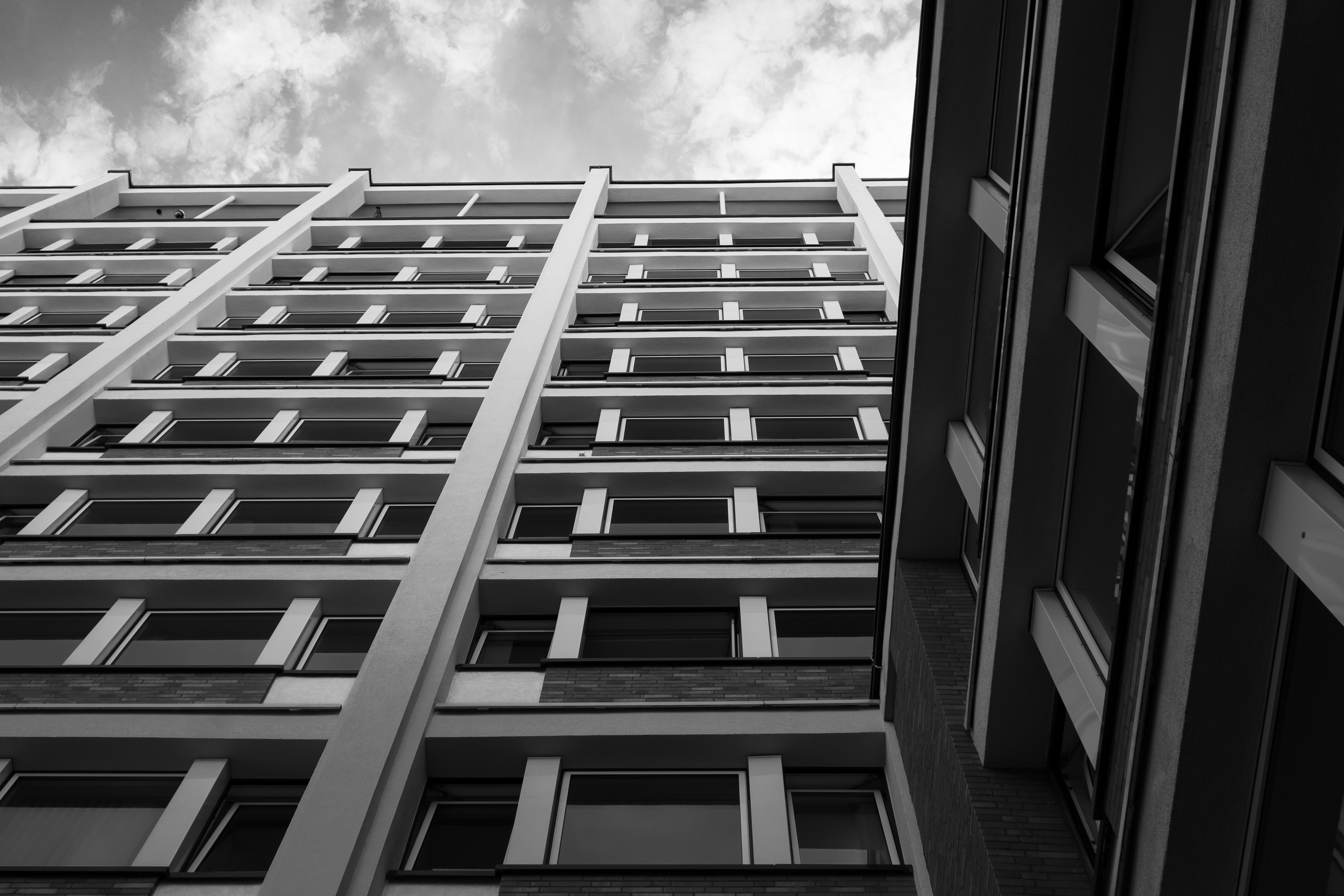 Low angle view of a high-rise building against a cloudy sky in black and white.