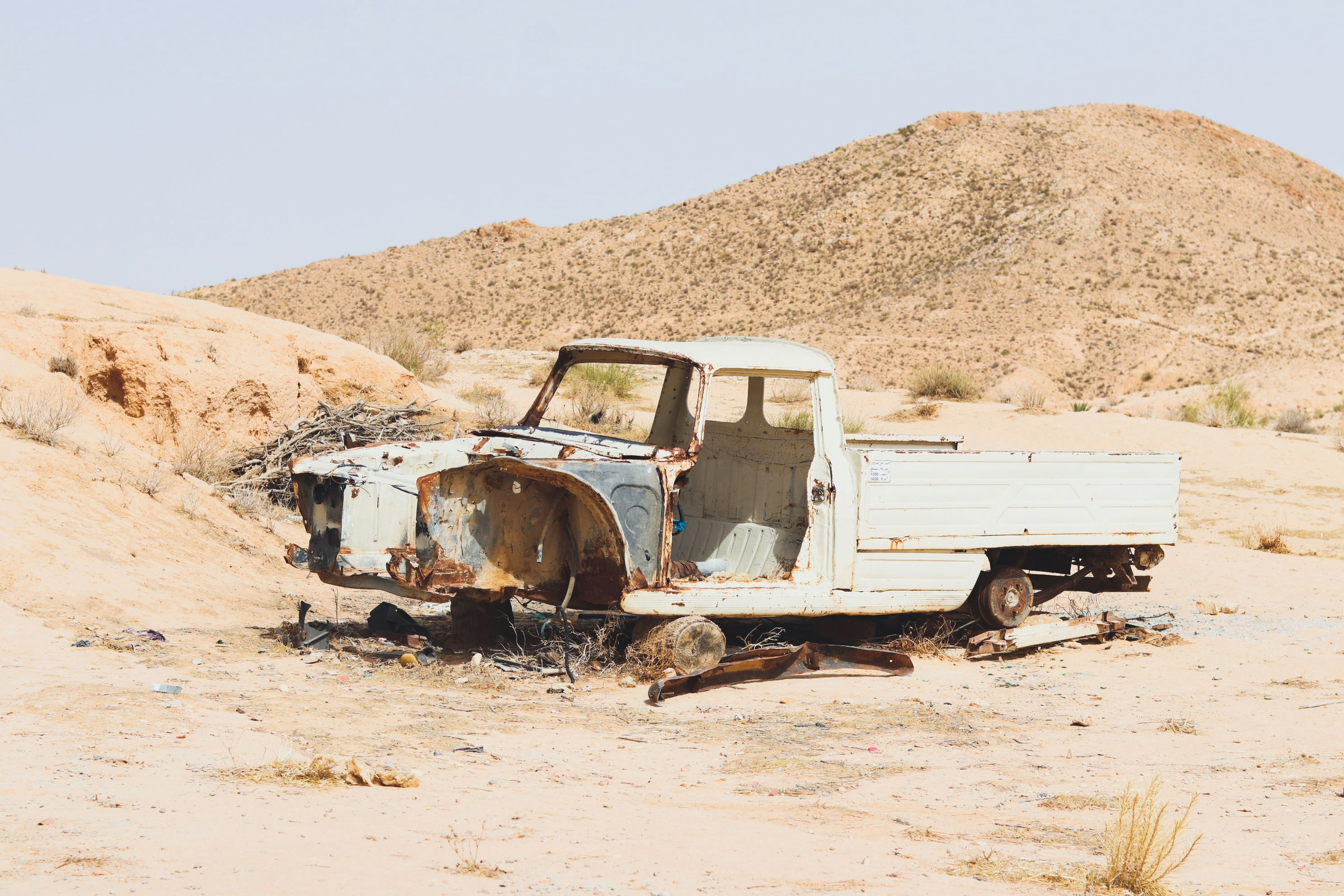 Abandoned truck rusting away in a desolate desert landscape, surrounded by rolling hills and sparse vegetation.