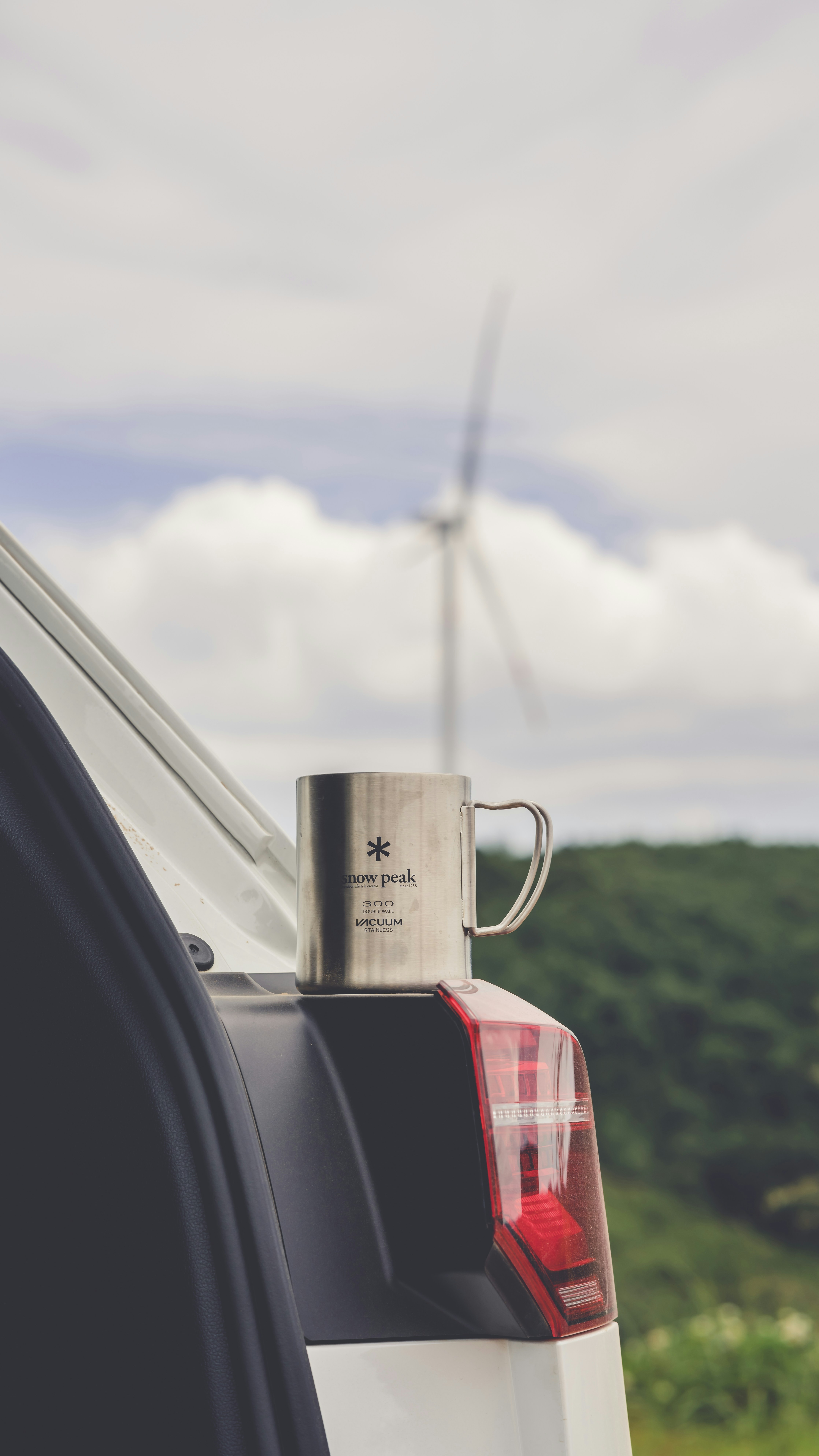 Stainless Mug on a Tailgate, Framed by a Distant Wind Turbine
