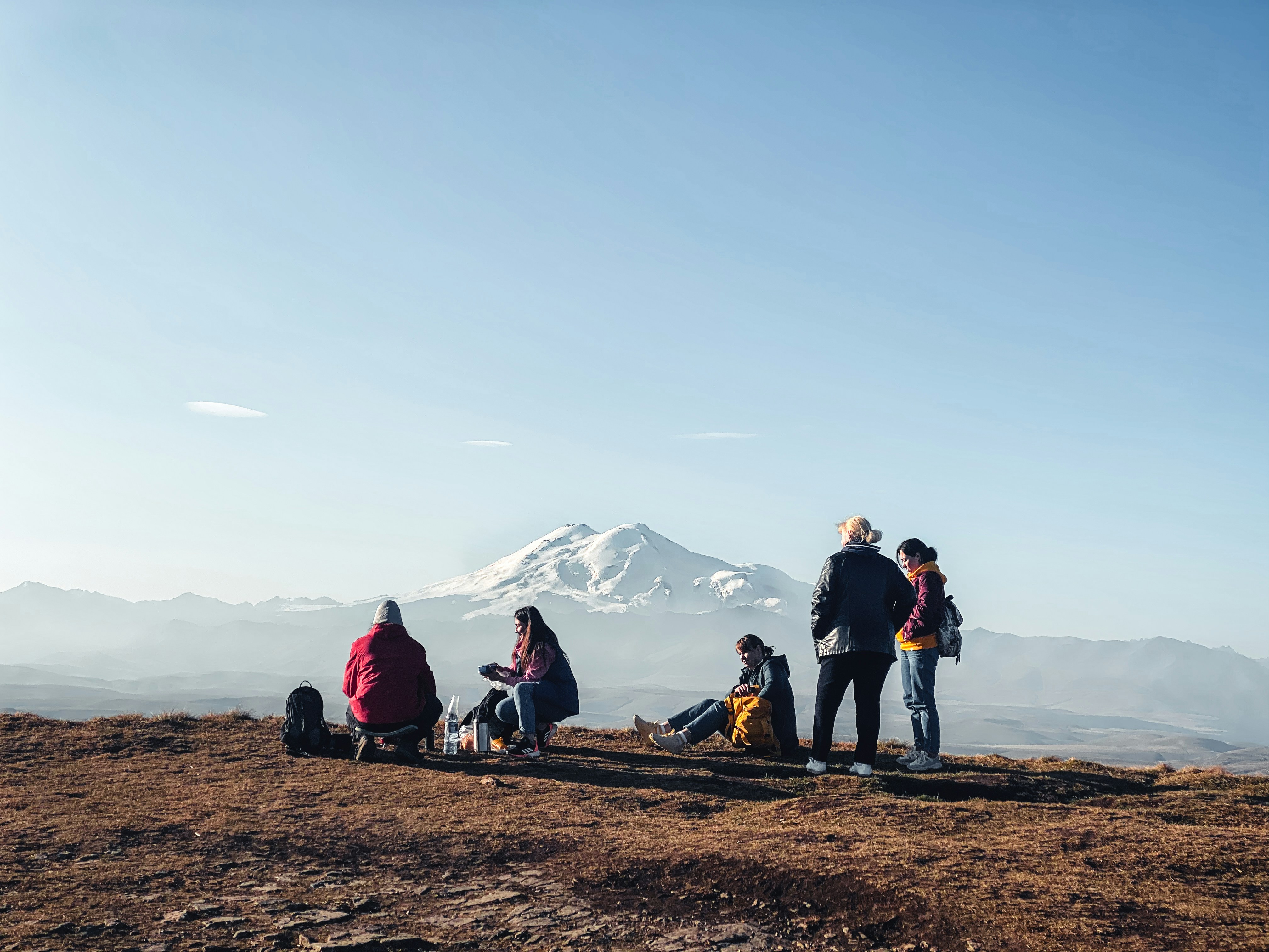 Group of hikers resting with distant snow-capped peak under clear sky