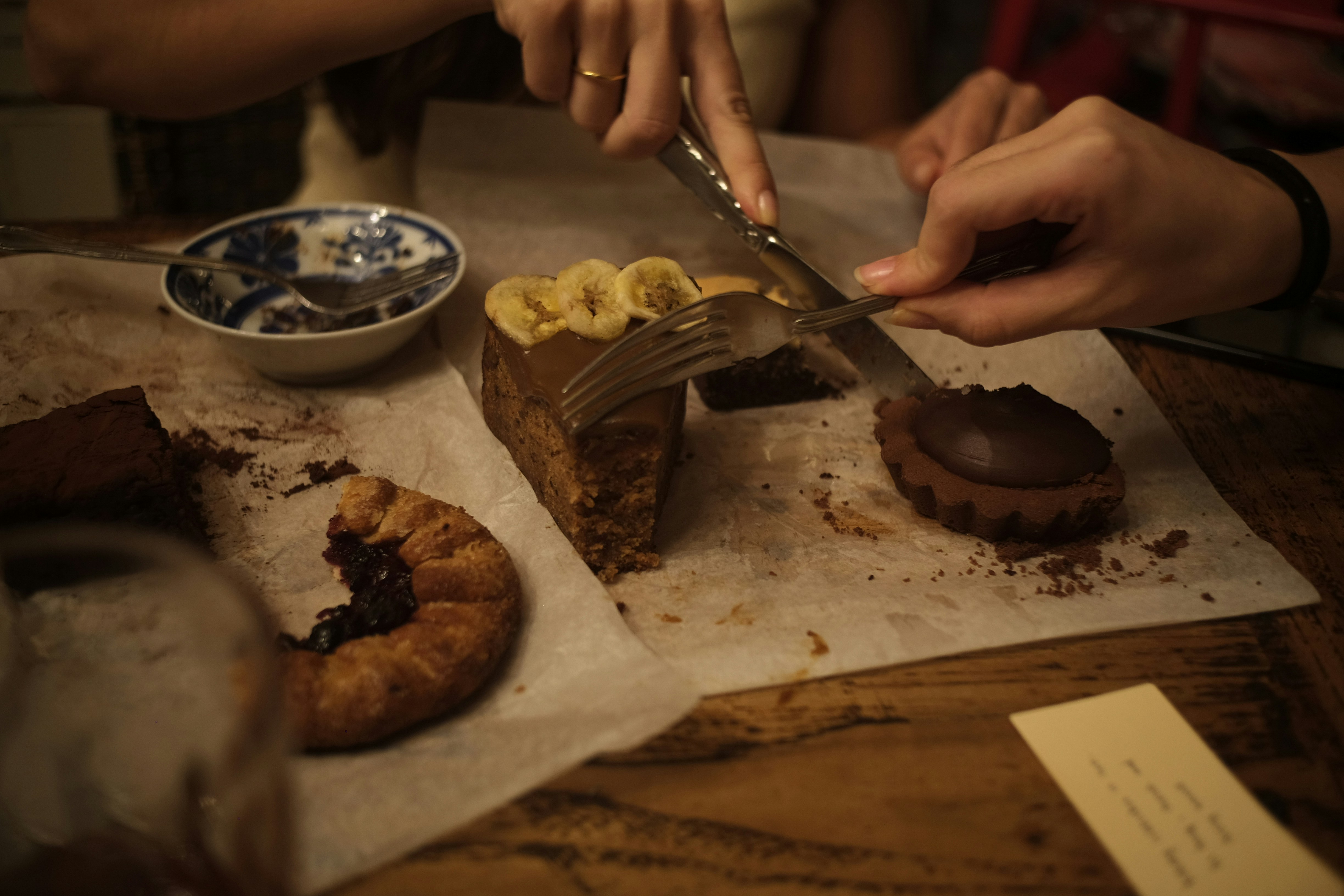 Banana-Topped Cake Slice Being Cut Under Warm Bakery Lighting