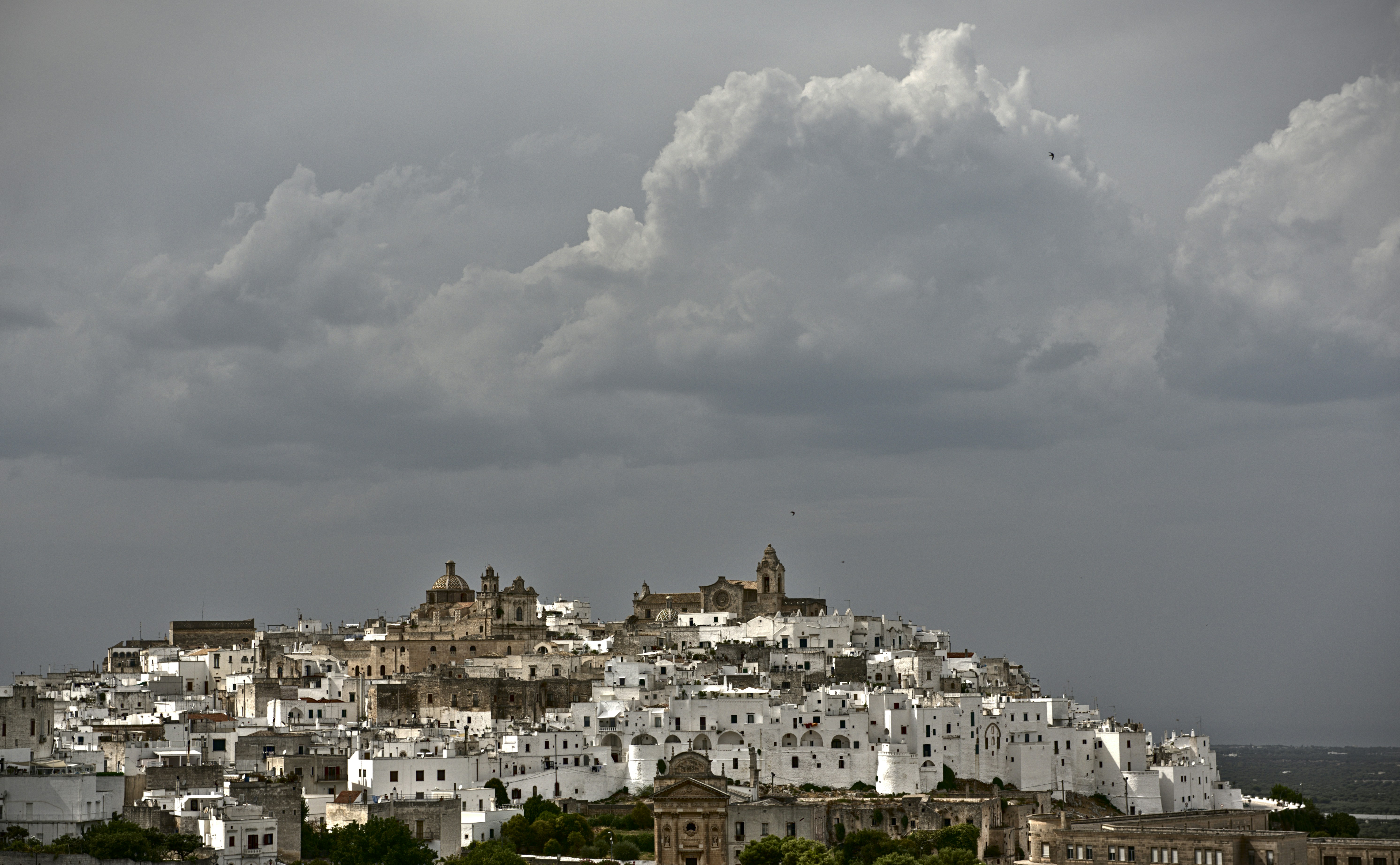 Historic whitewashed buildings of a hilltop town contrast against a dramatic, cloudy sky. The scene evokes a sense of tranquility and timelessness.