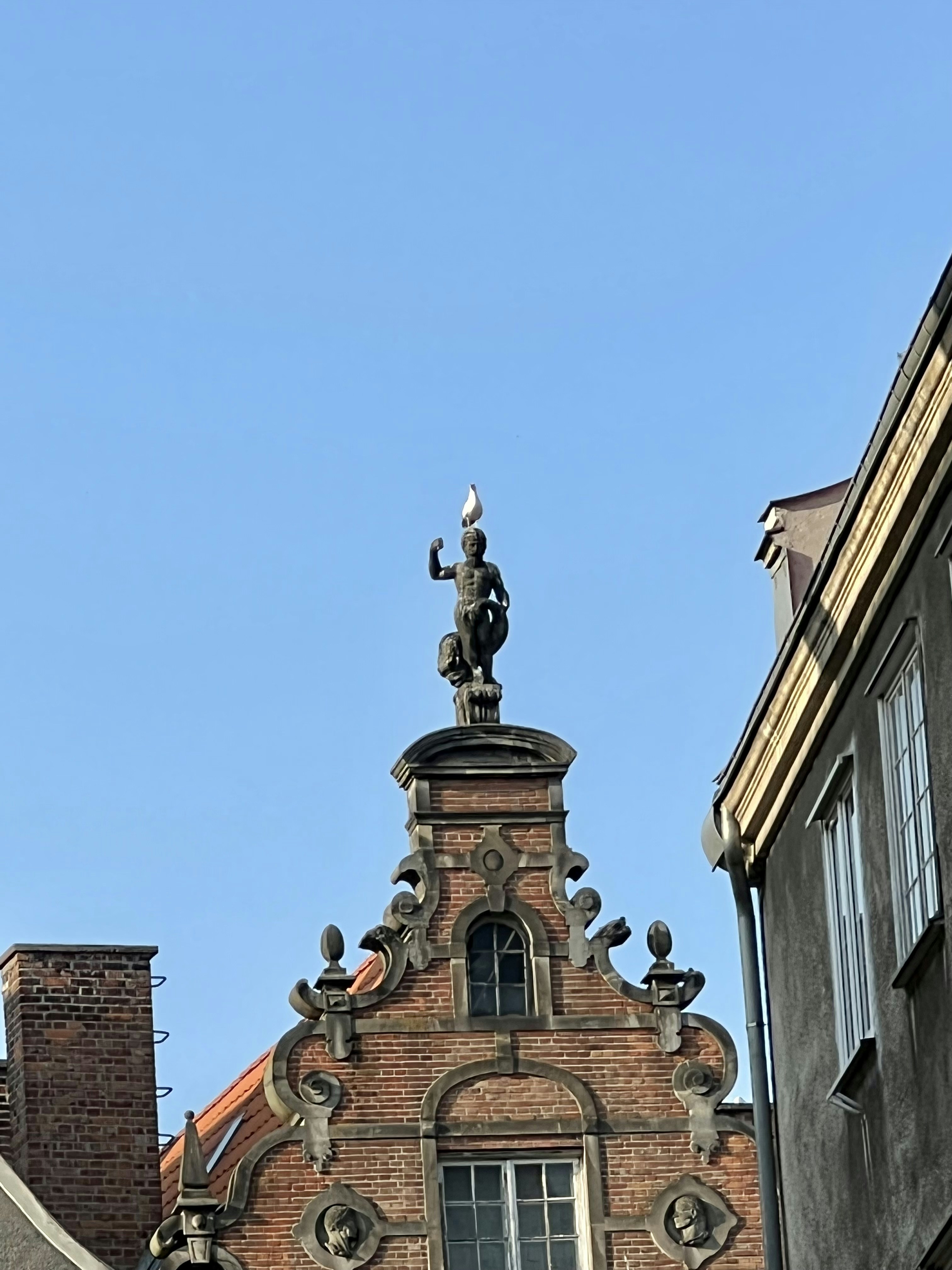 Crowned Gable: Statue Above Ornate Brickwork Under a Clear Sky