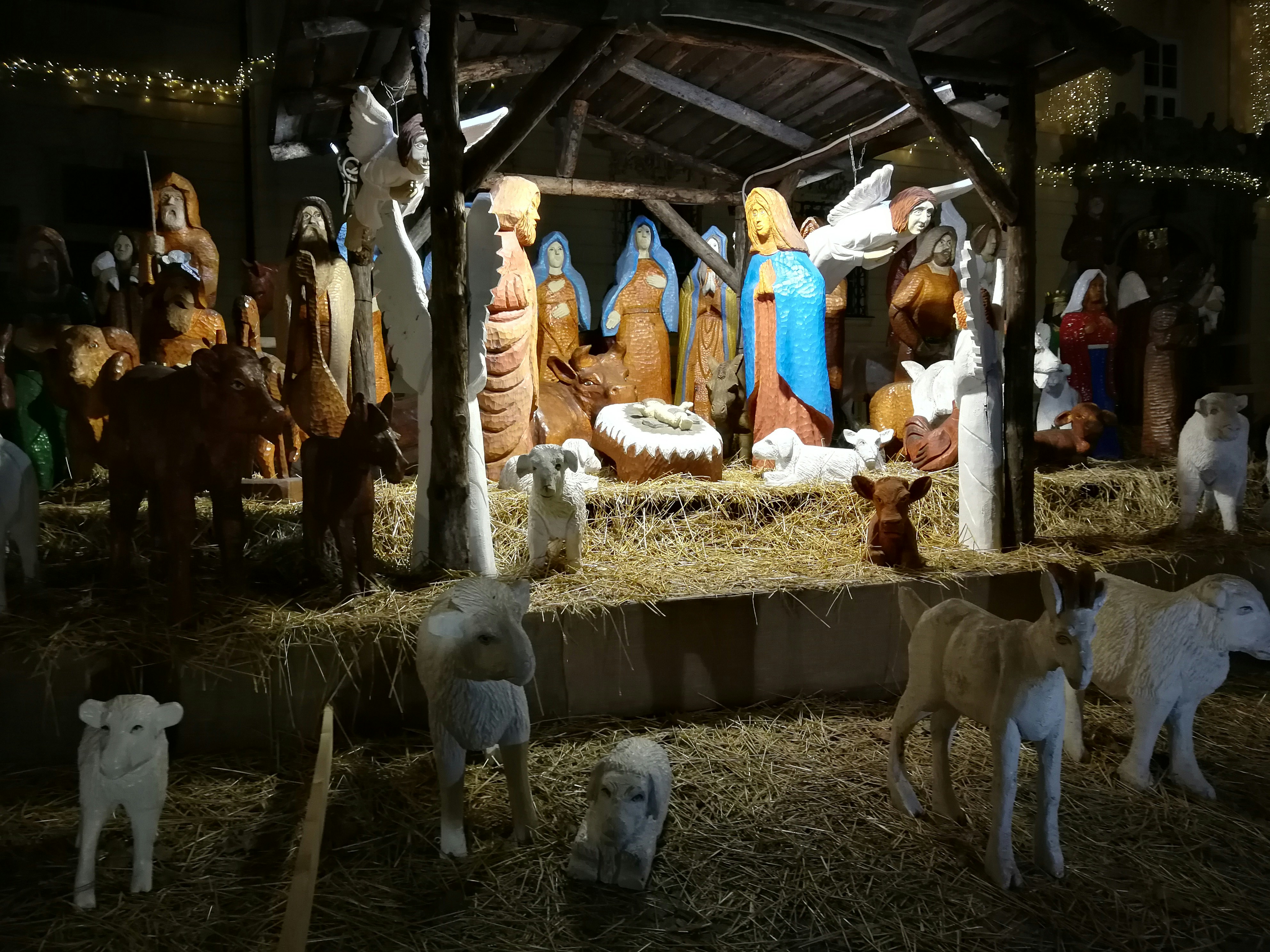 Nativity scene featuring intricately crafted figures of Mary, Joseph, and various animals, illuminated softly in a festive setting.