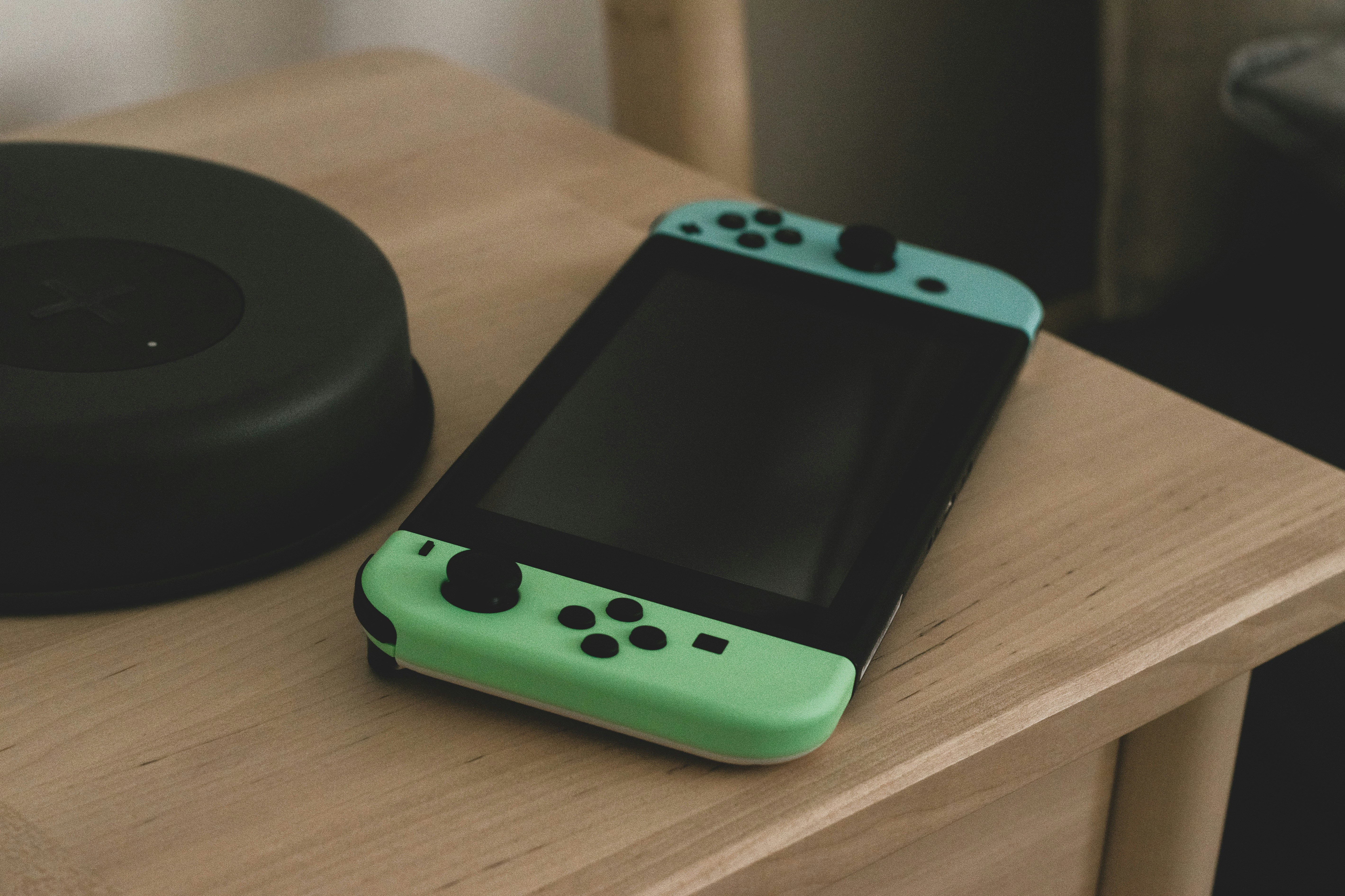 Nintendo Switch resting on a wooden table next to a round black object, showcasing a minimalist gaming setup.