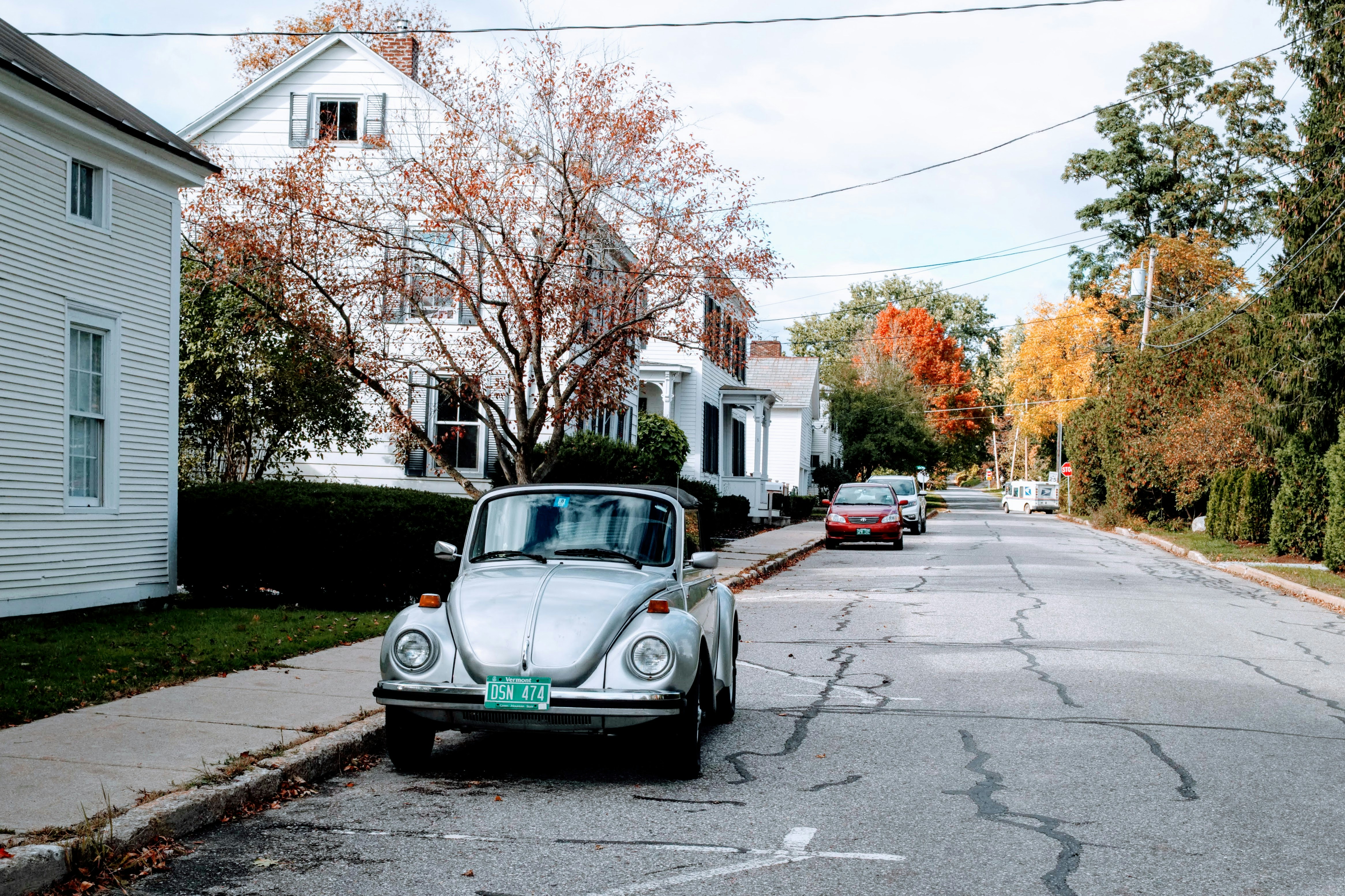 Classic silver car parked on a quiet tree-lined street with autumn foliage.