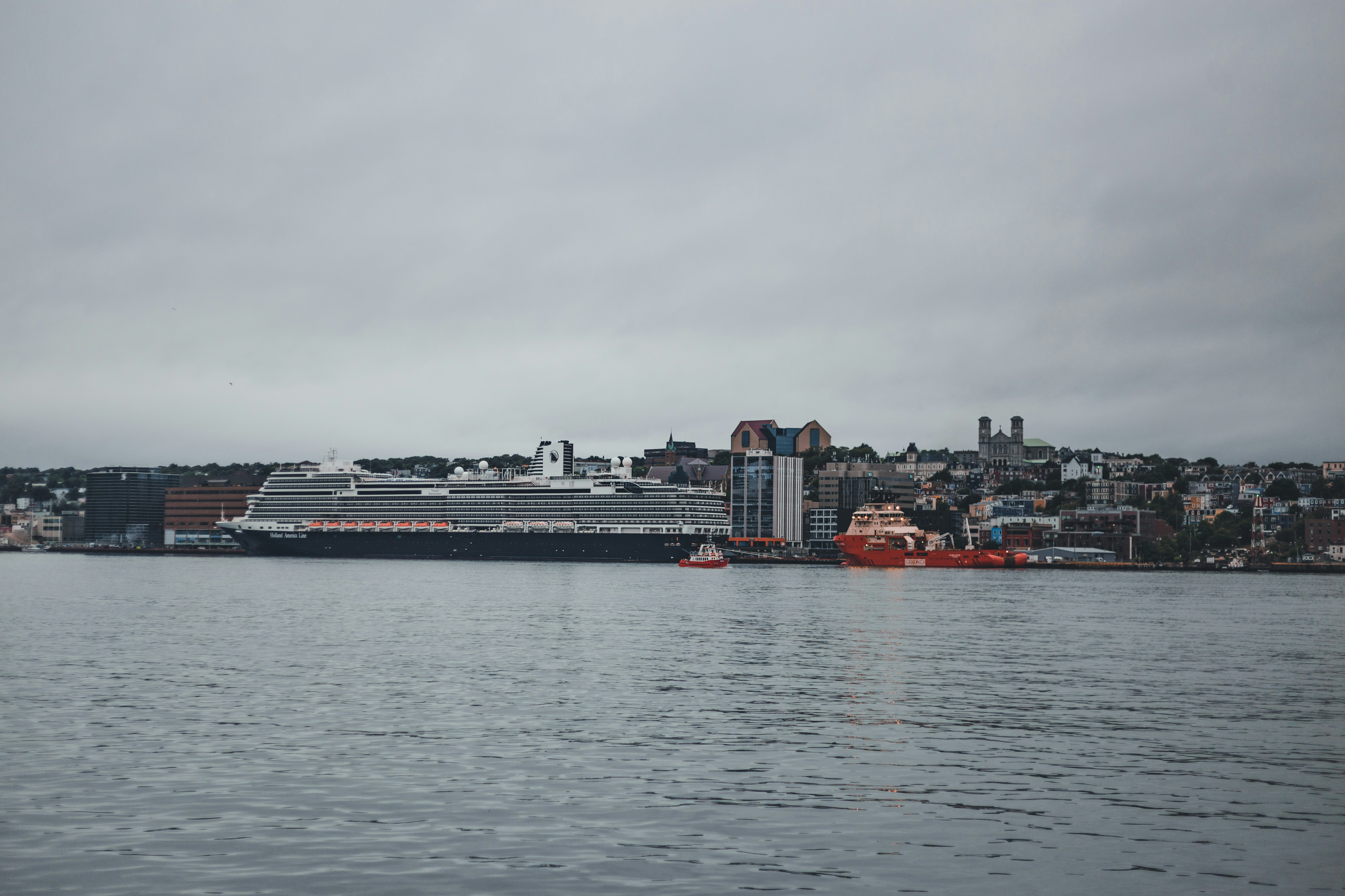 Overcast Harbor: Cruise Ship, Red Tug, and a City by the Water