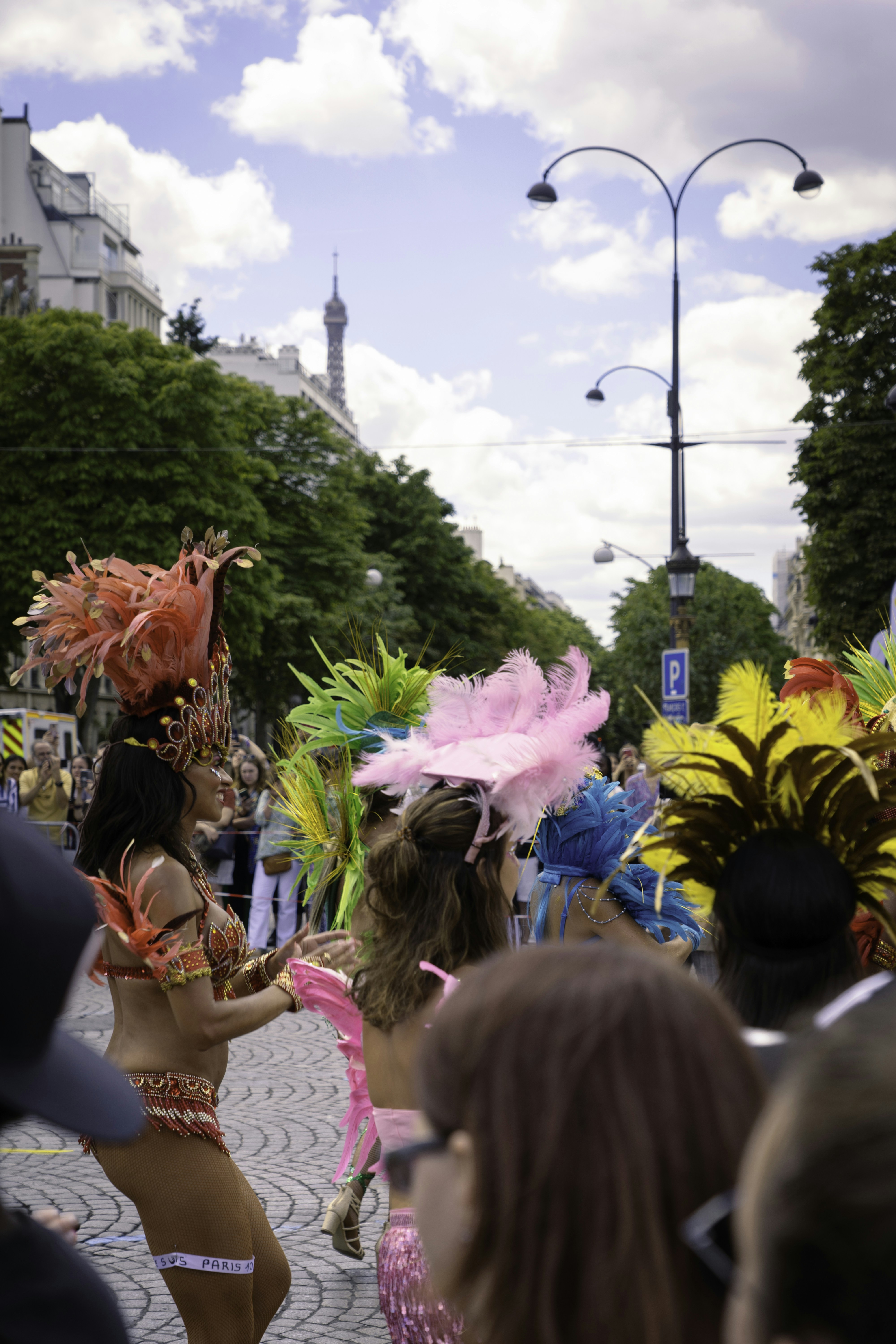 Dancers in colorful costumes celebrate during a lively parade, with the Eiffel Tower visible in the background. The festive atmosphere captures the spirit of cultural celebration.