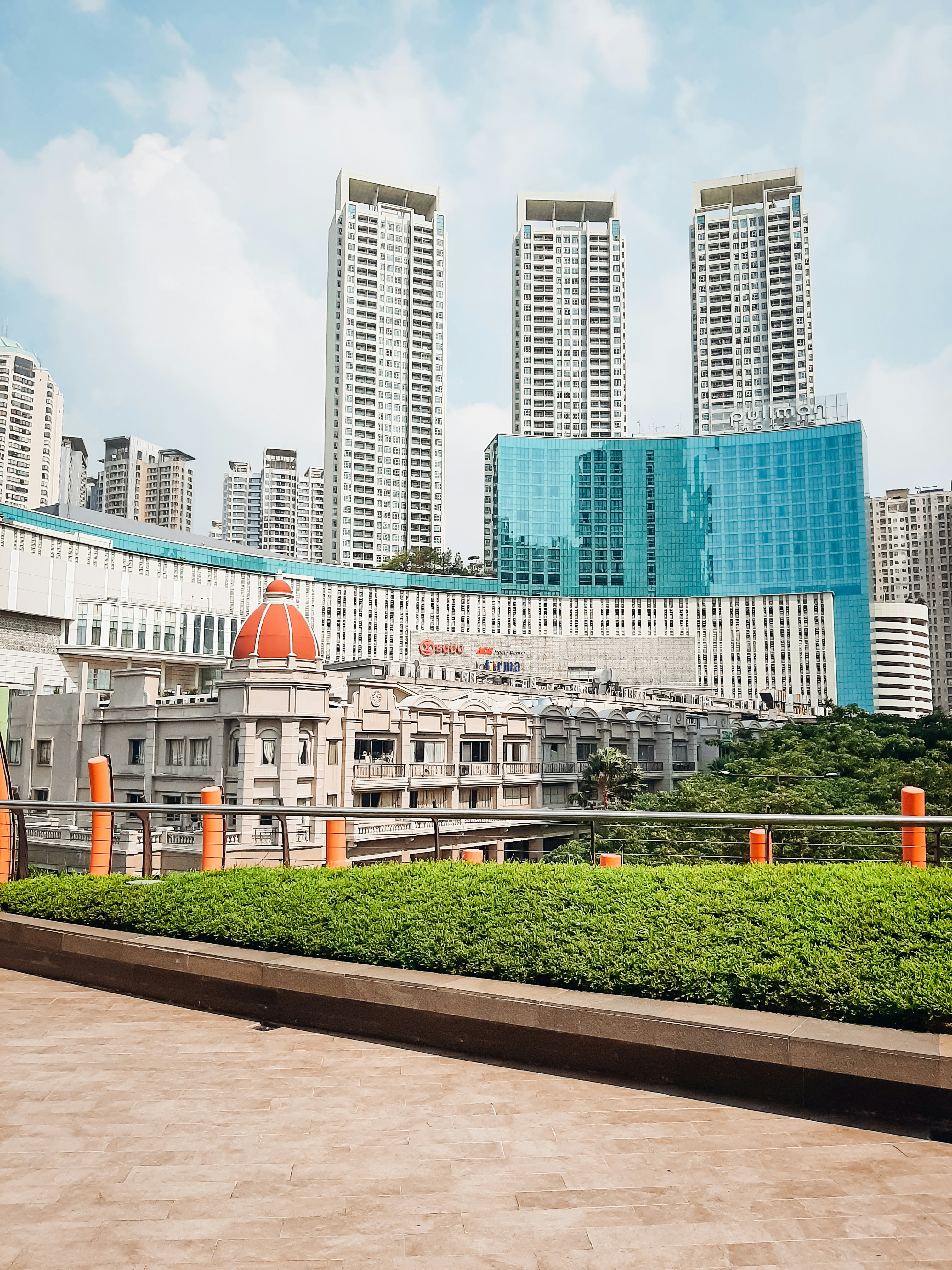 Modern skyscrapers rise above a lush green terrace, showcasing the contrast between urban architecture and nature. The vibrant colors and clean lines highlight the city's dynamic landscape.