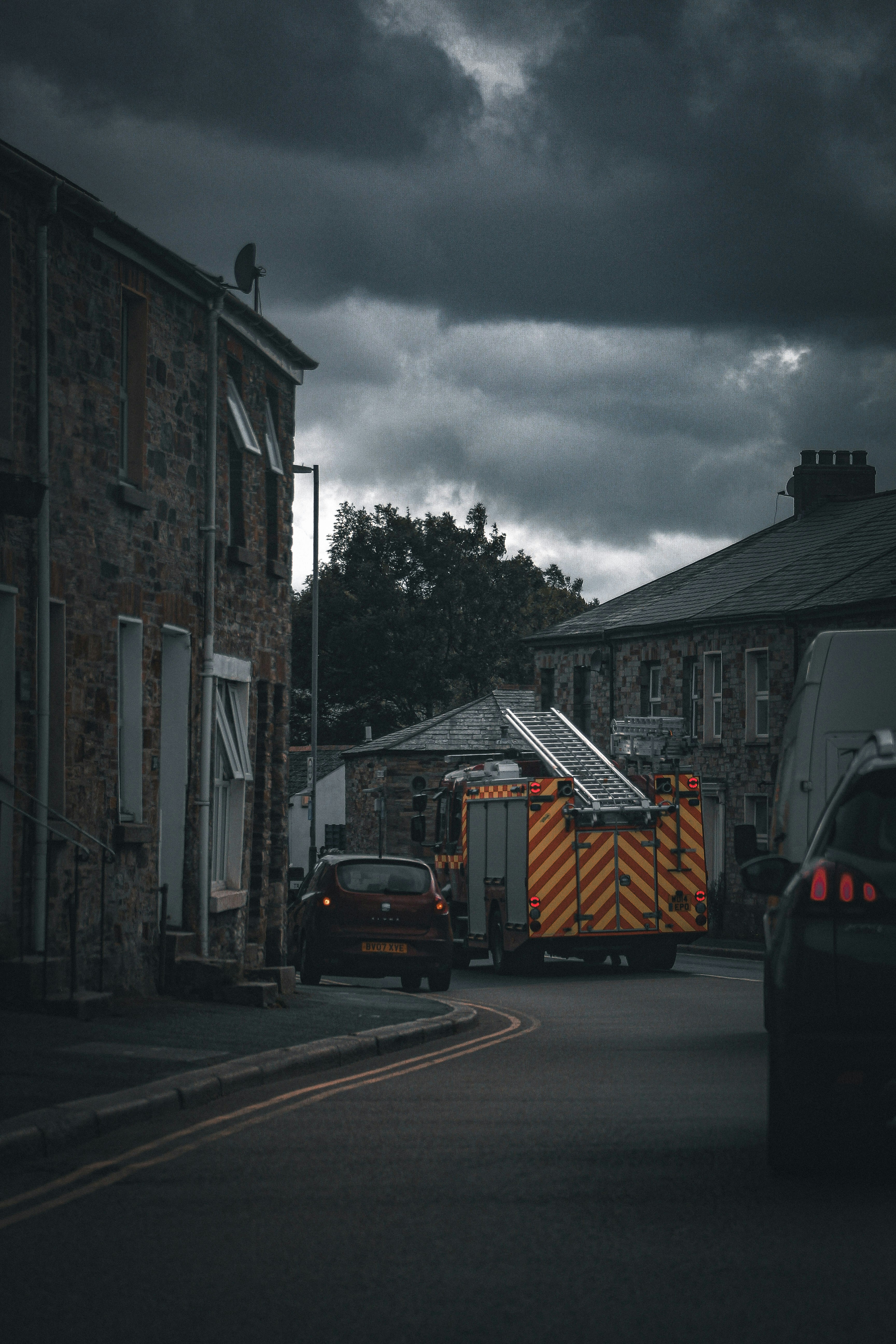 Fire truck navigating a narrow street surrounded by stone buildings under a moody sky.